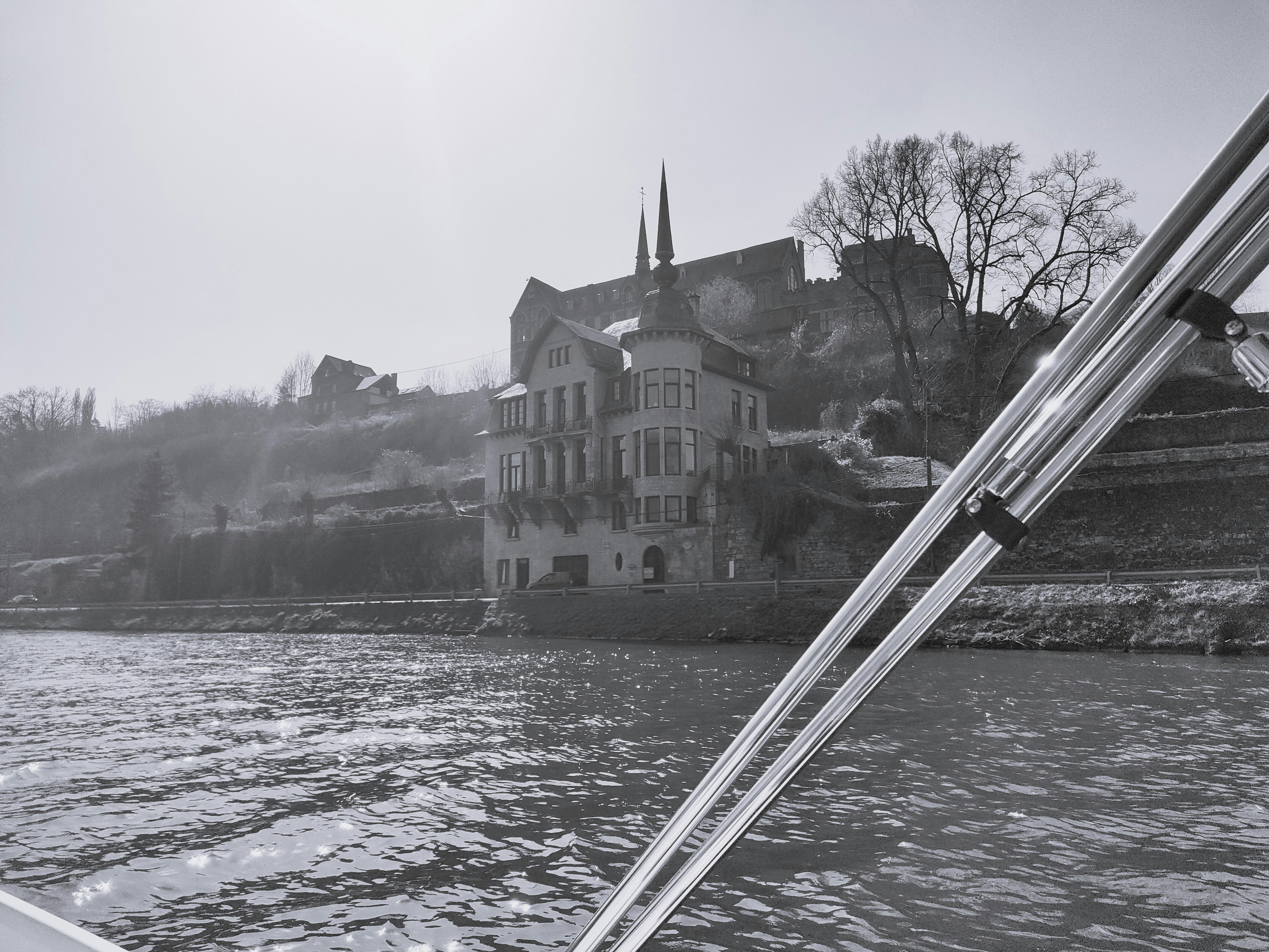 Historic riverside building with spires viewed from a boat under a cloudy sky.
