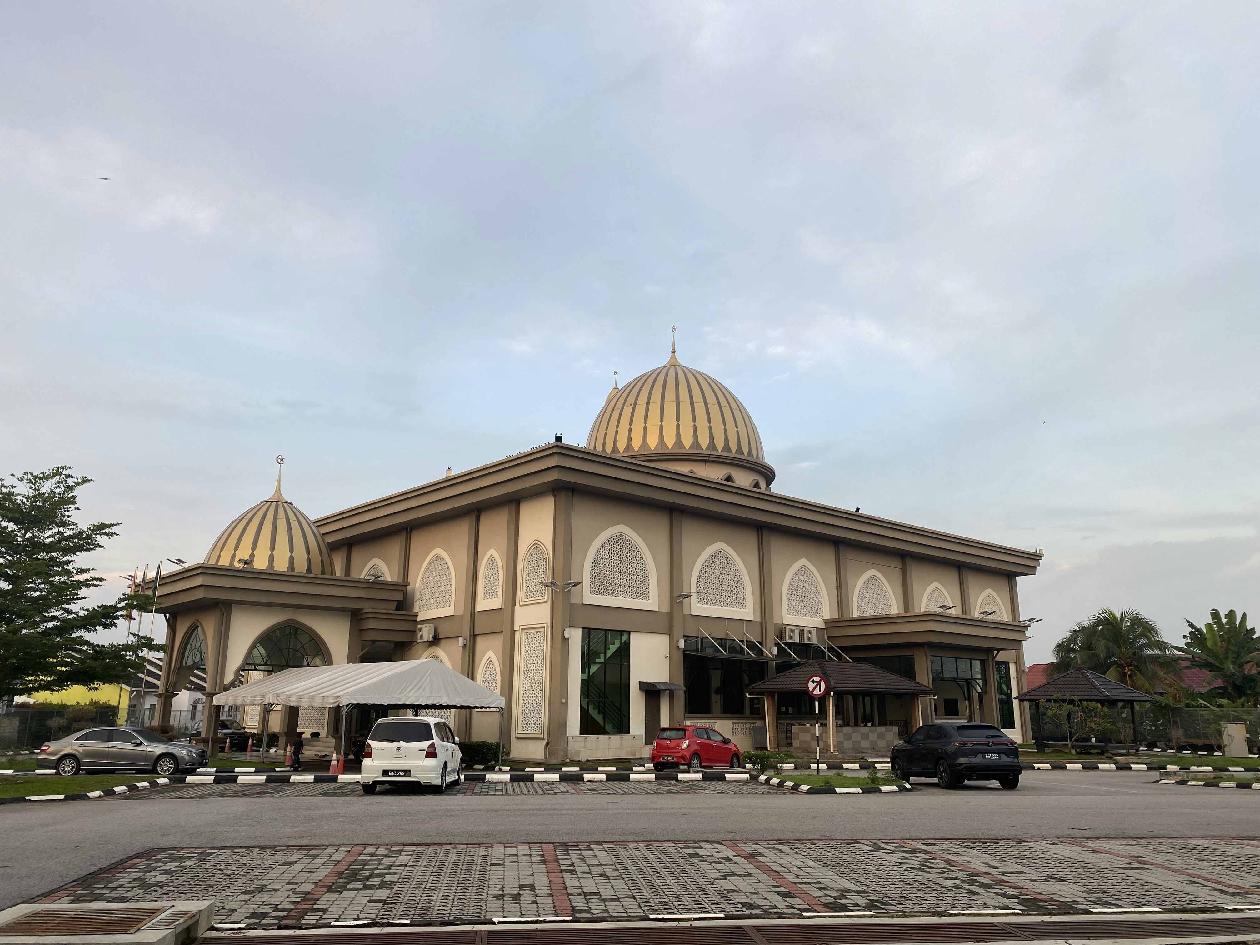 Modern mosque with golden domes against a cloudy sky.
