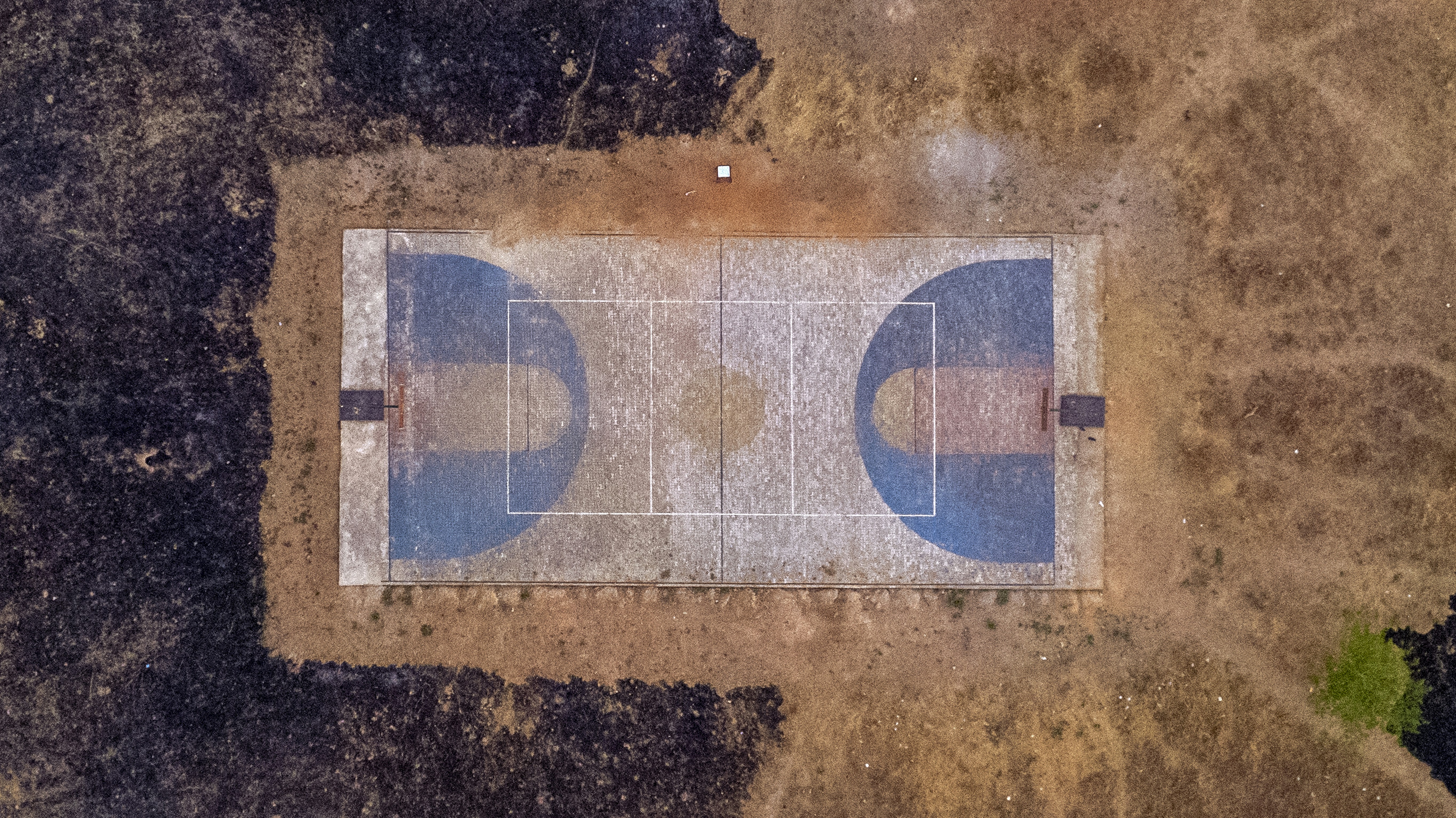Blue-Hued Court in Dry Light: Aerial View of a Compact Outdoor Basketball Court