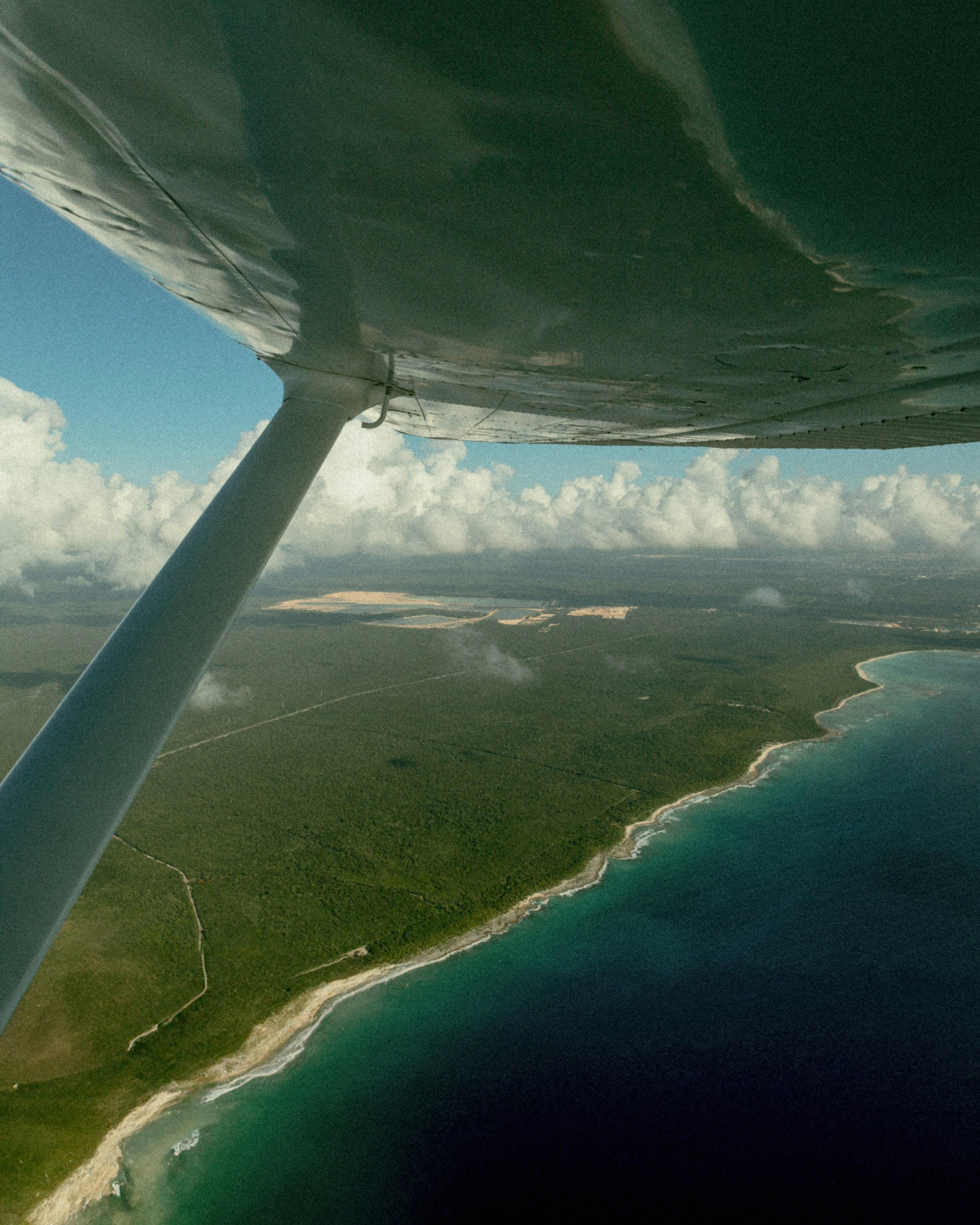 Aerial view of a coastline with lush greenery and azure waters under a plane wing.