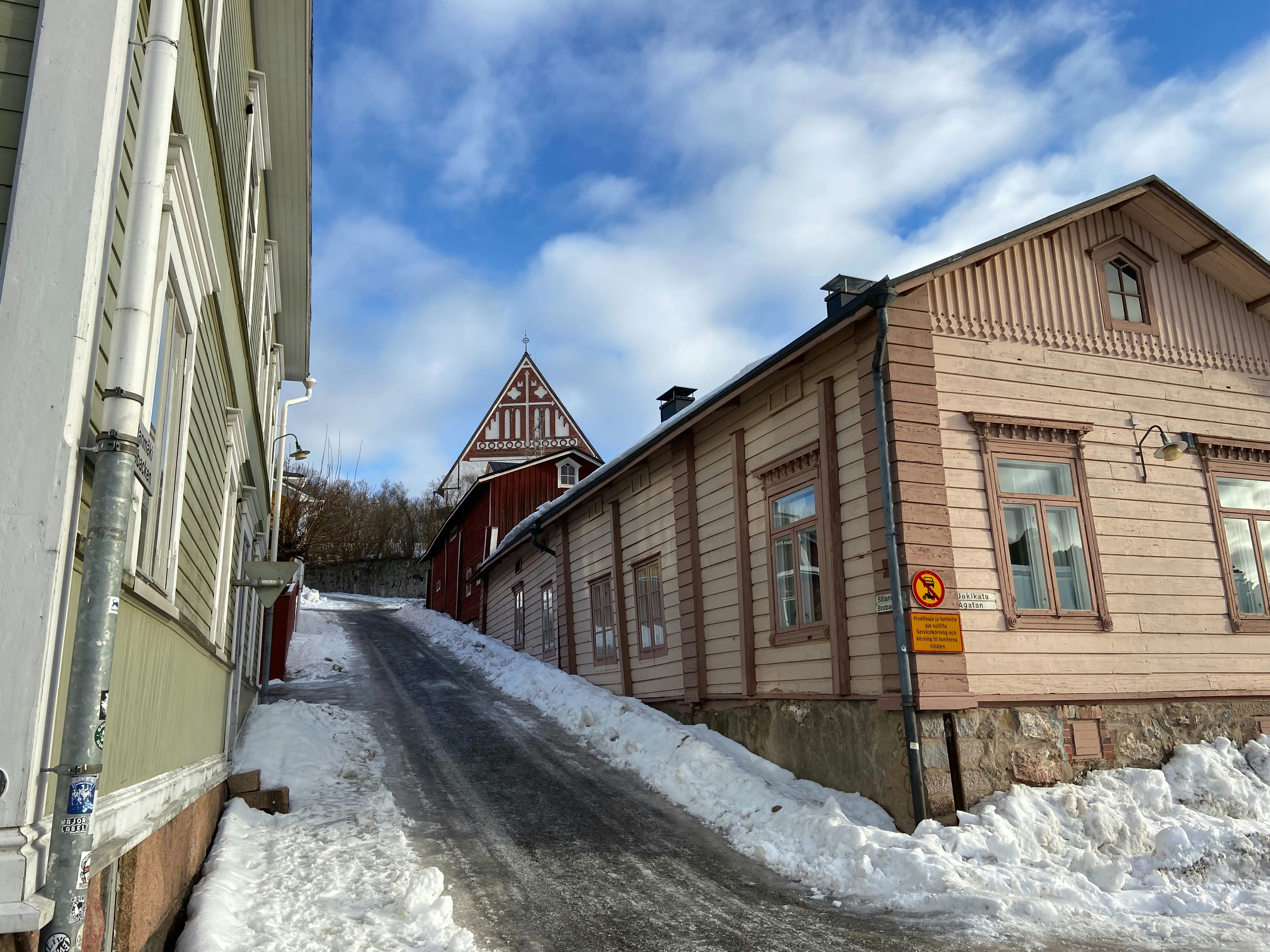 Charming wooden buildings line a snow-covered street under a vibrant blue sky.