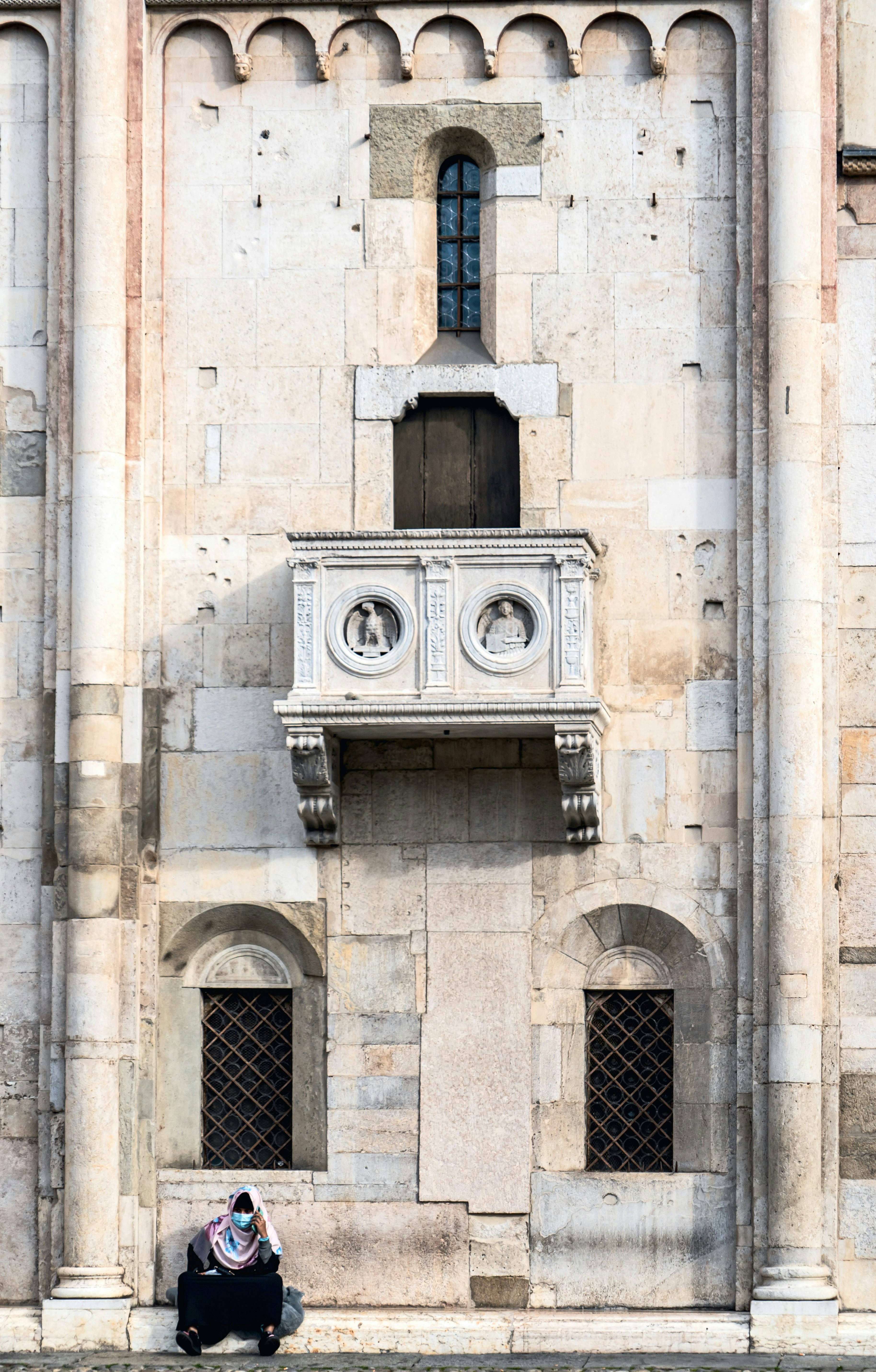 Quiet Figure at the Foot of a Carved Facade Beneath a Stone Balcony
