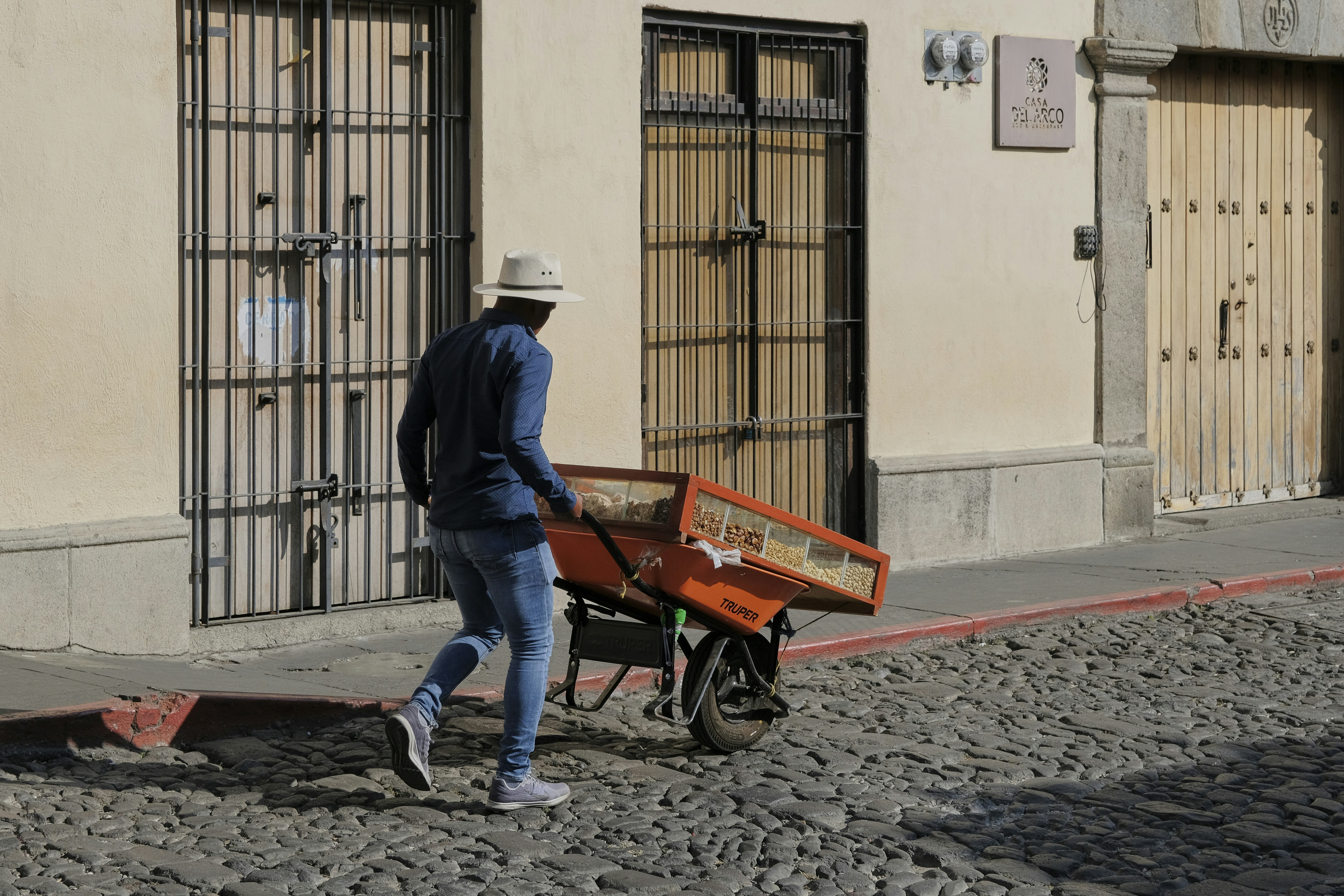 A man pushing a wheelbarrow down a street photo – Free Building Image ...