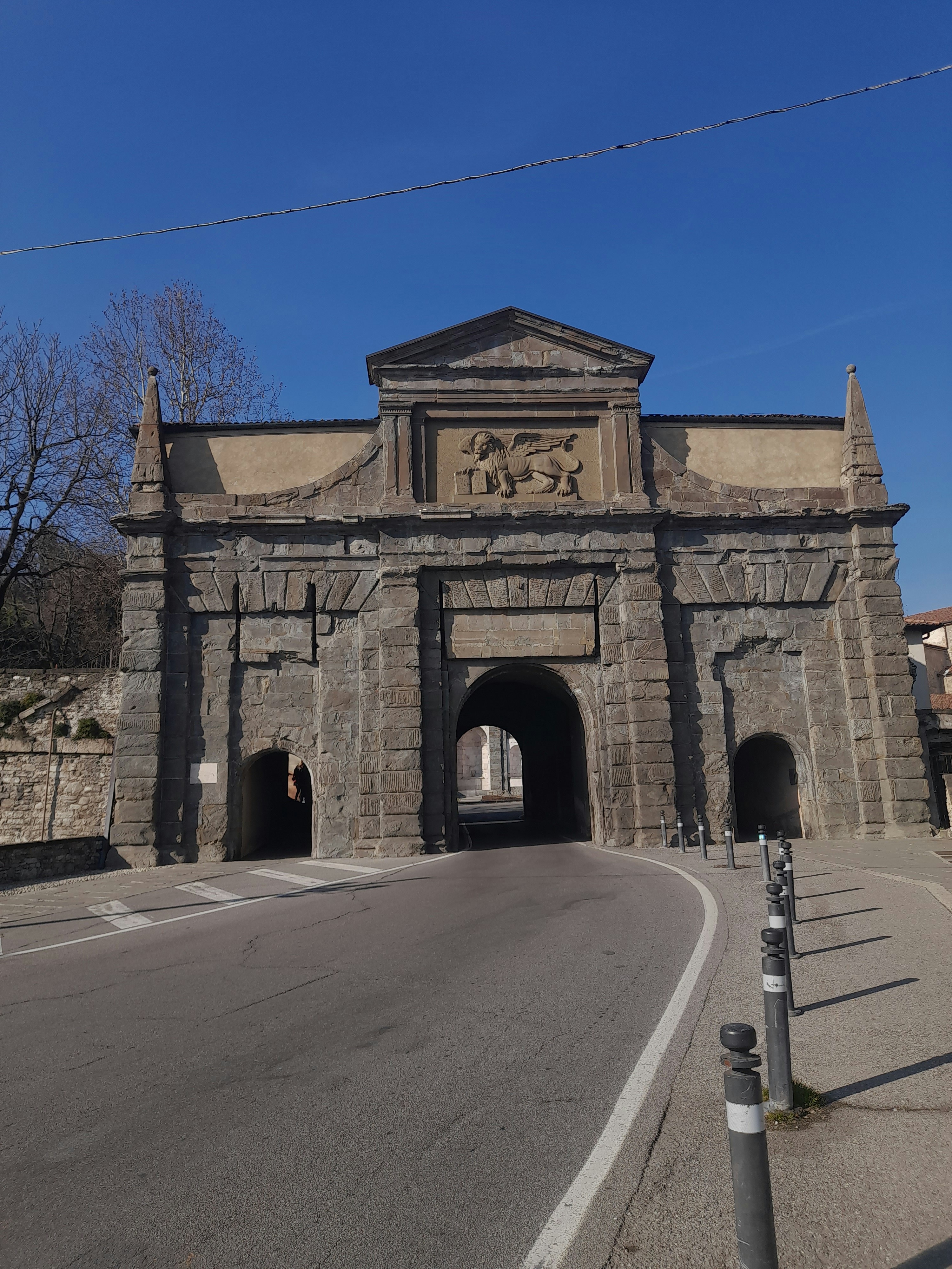Stone gateway with three arches and intricate carvings under a bright blue sky.