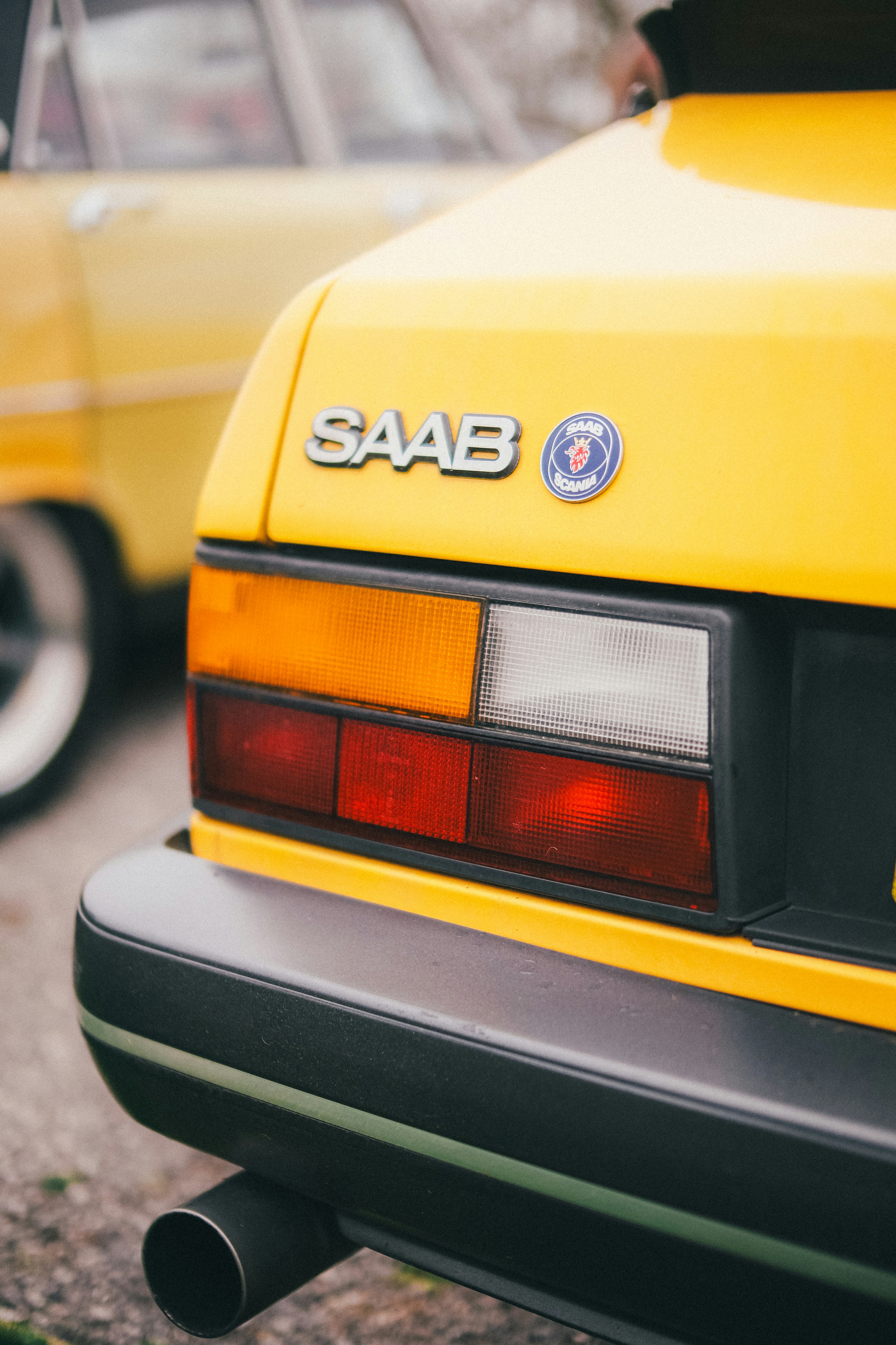 Close-up of a yellow Saab car's rear emblem and taillights, showcasing its vintage design and distinctive features.