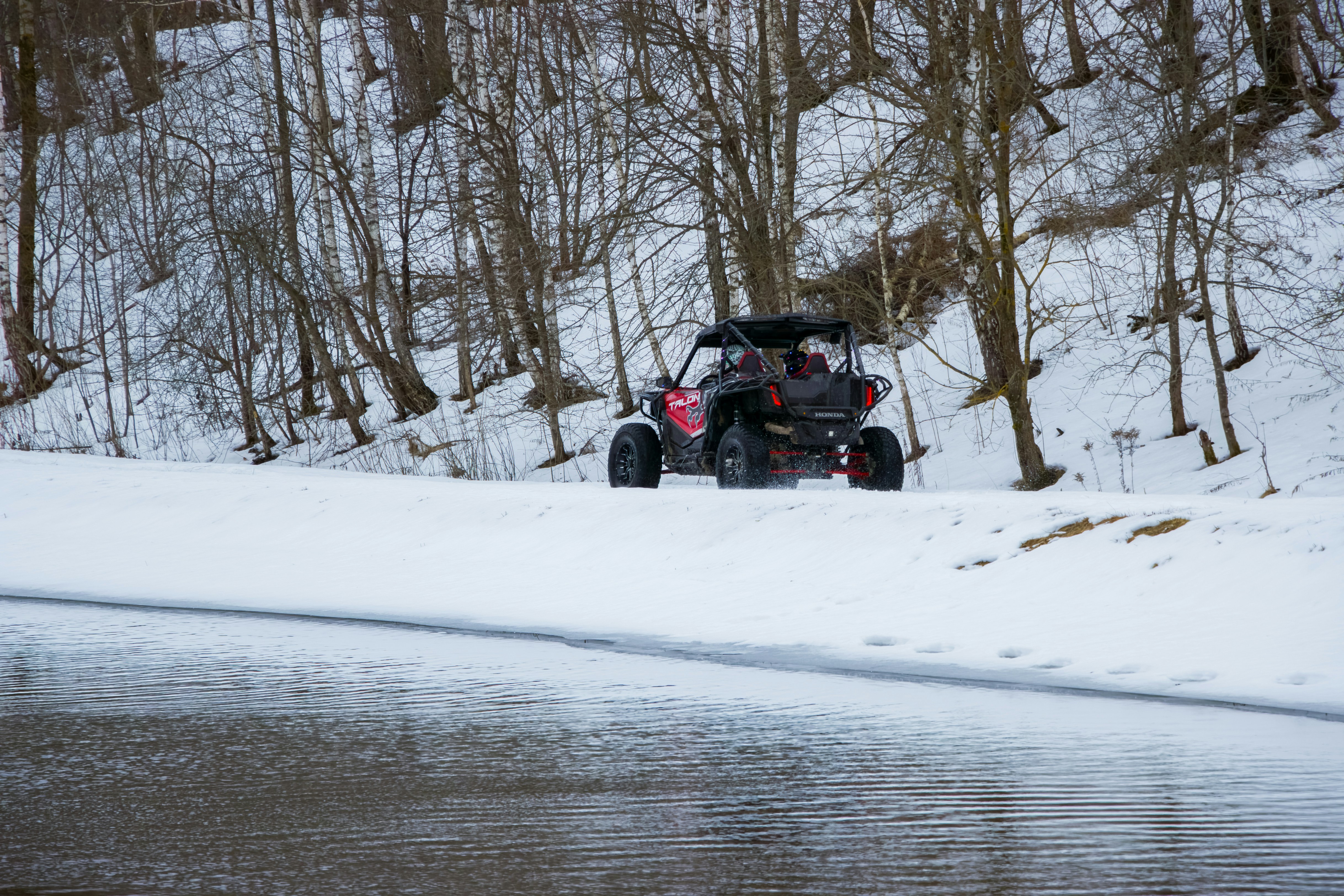 Red UTV Pauses on a Snow-Blanketed Bank by a Quiet Frozen Shore