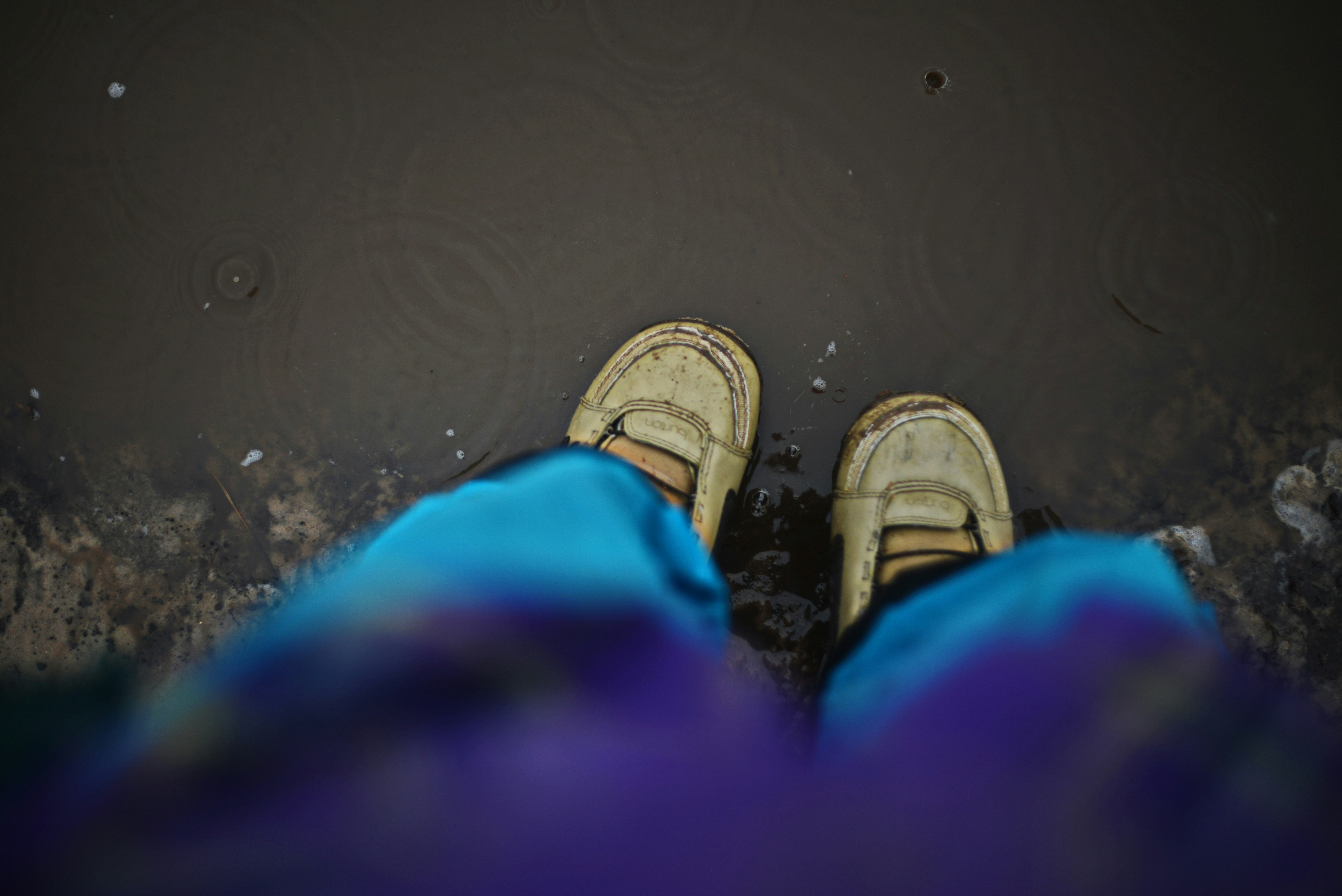 Yellow boots standing in a puddle with ripples on the water surface.