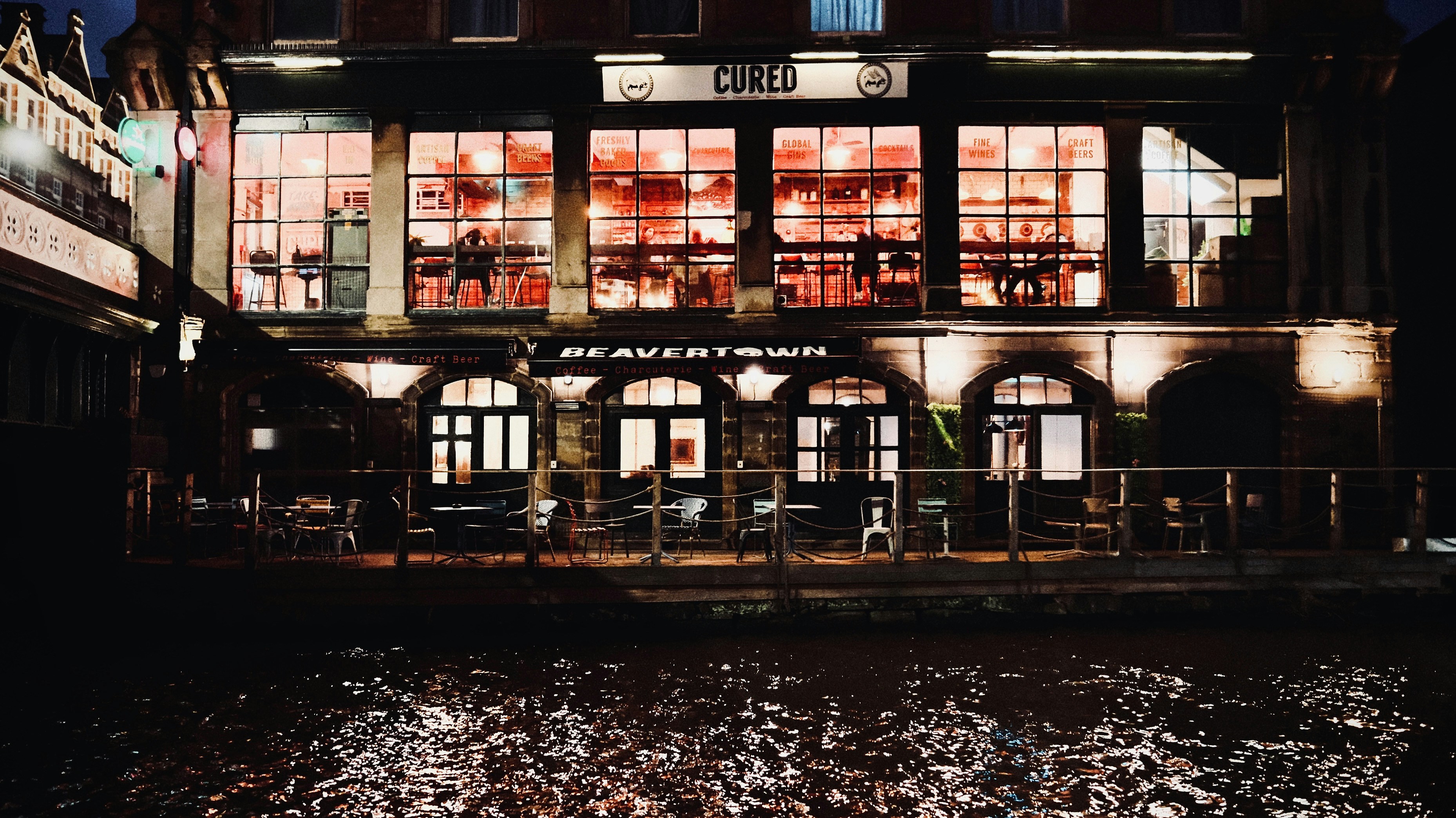 Illuminated riverside building with warm interior lights reflecting on the water at night.