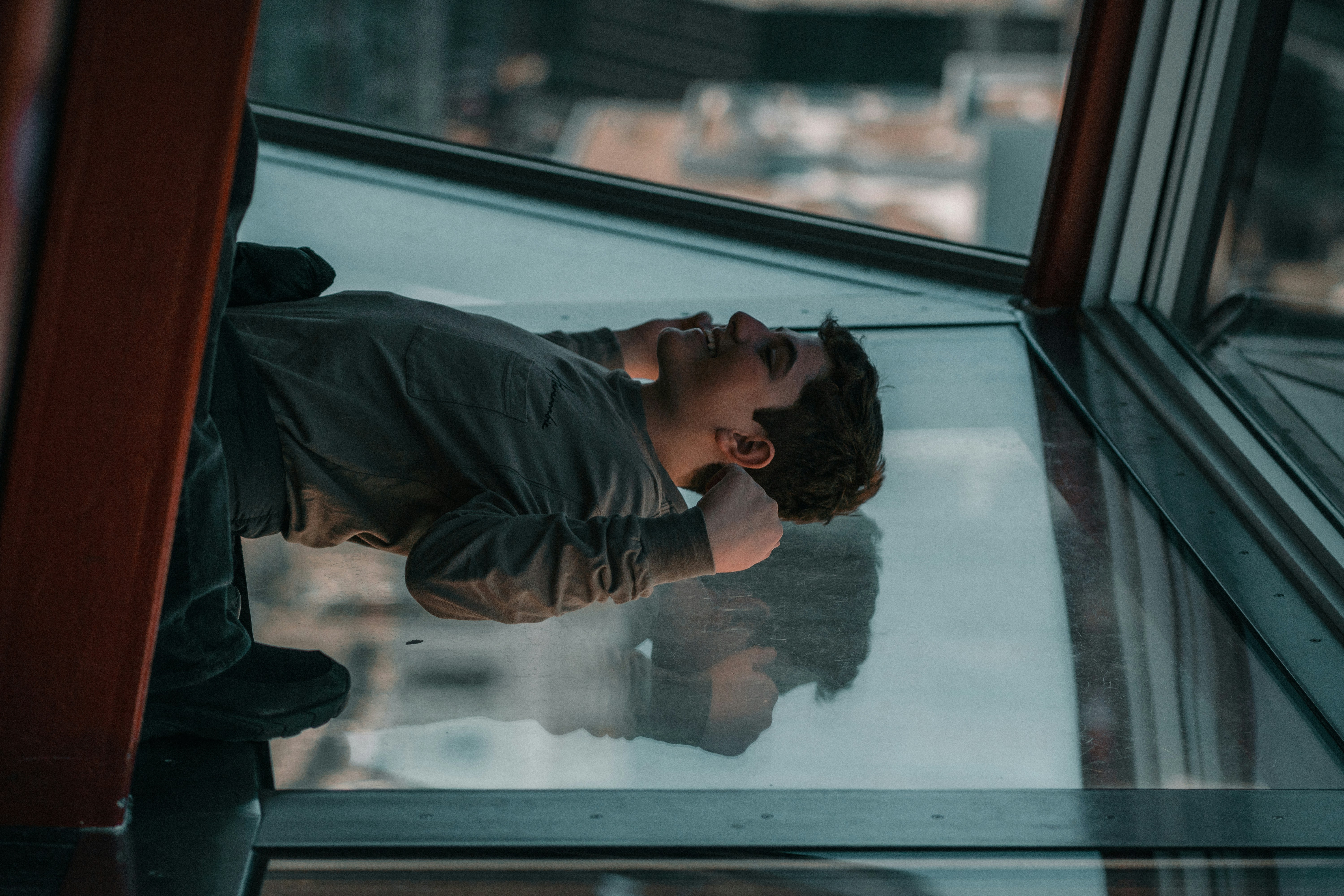A young man leaning against a window looking up photo – Free Laying ...