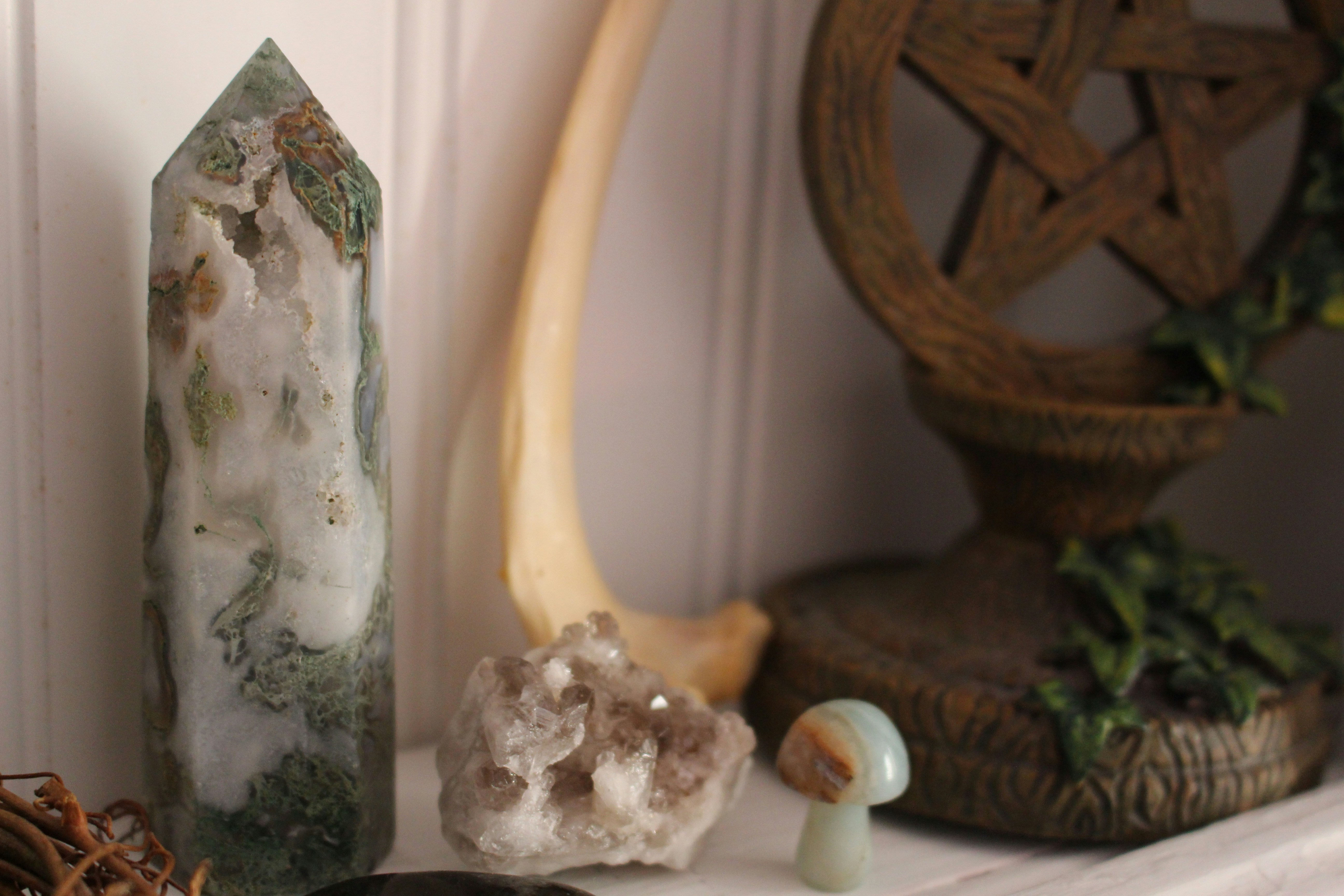 A green crystal tower stands tall beside a natural horn and a small, textured mineral cluster, creating an earthy and mystical display on a shelf.