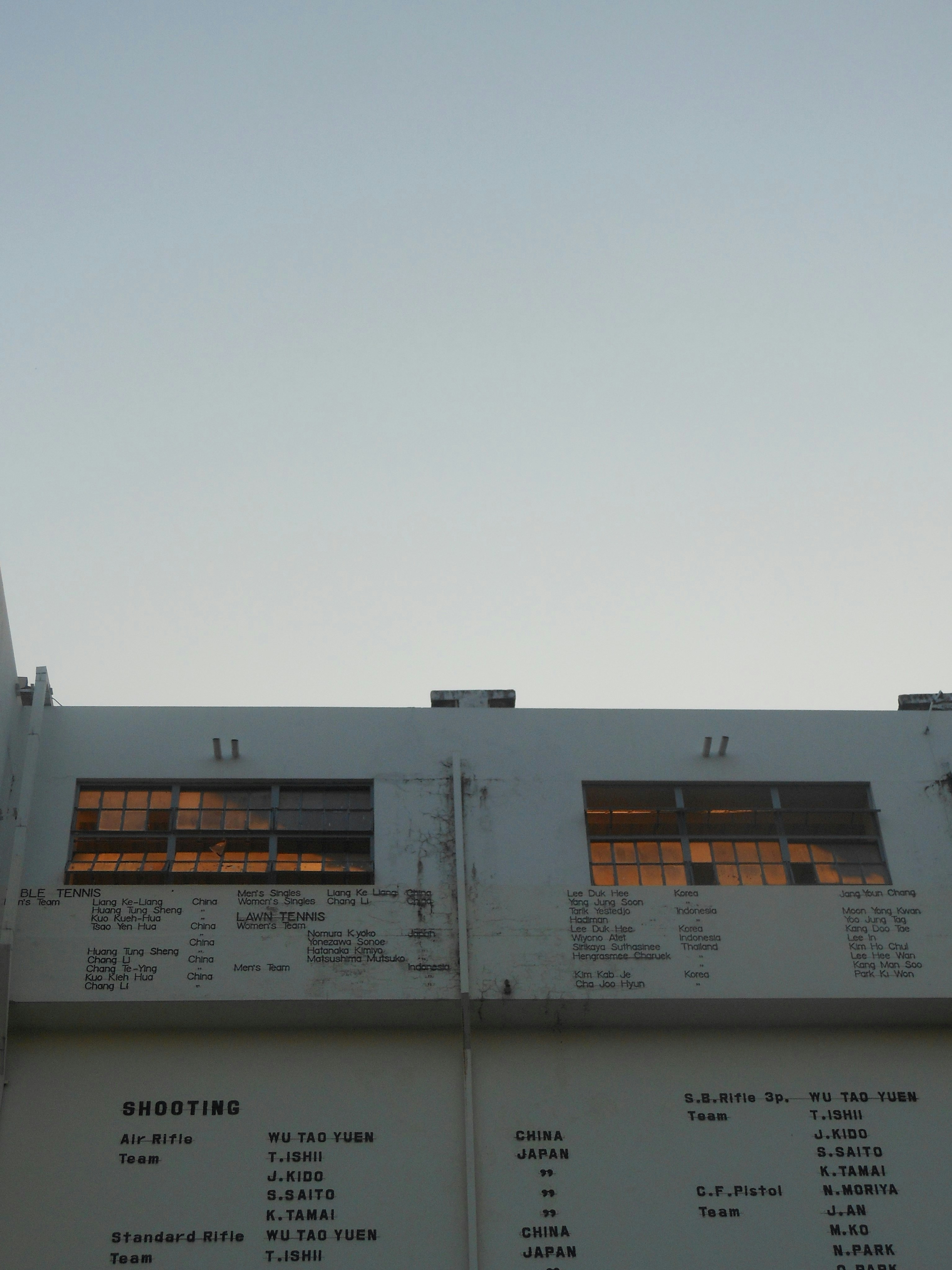 A white building facade displays dense rows of names and categories on its lower wall, set against a calm, pale blue sky.