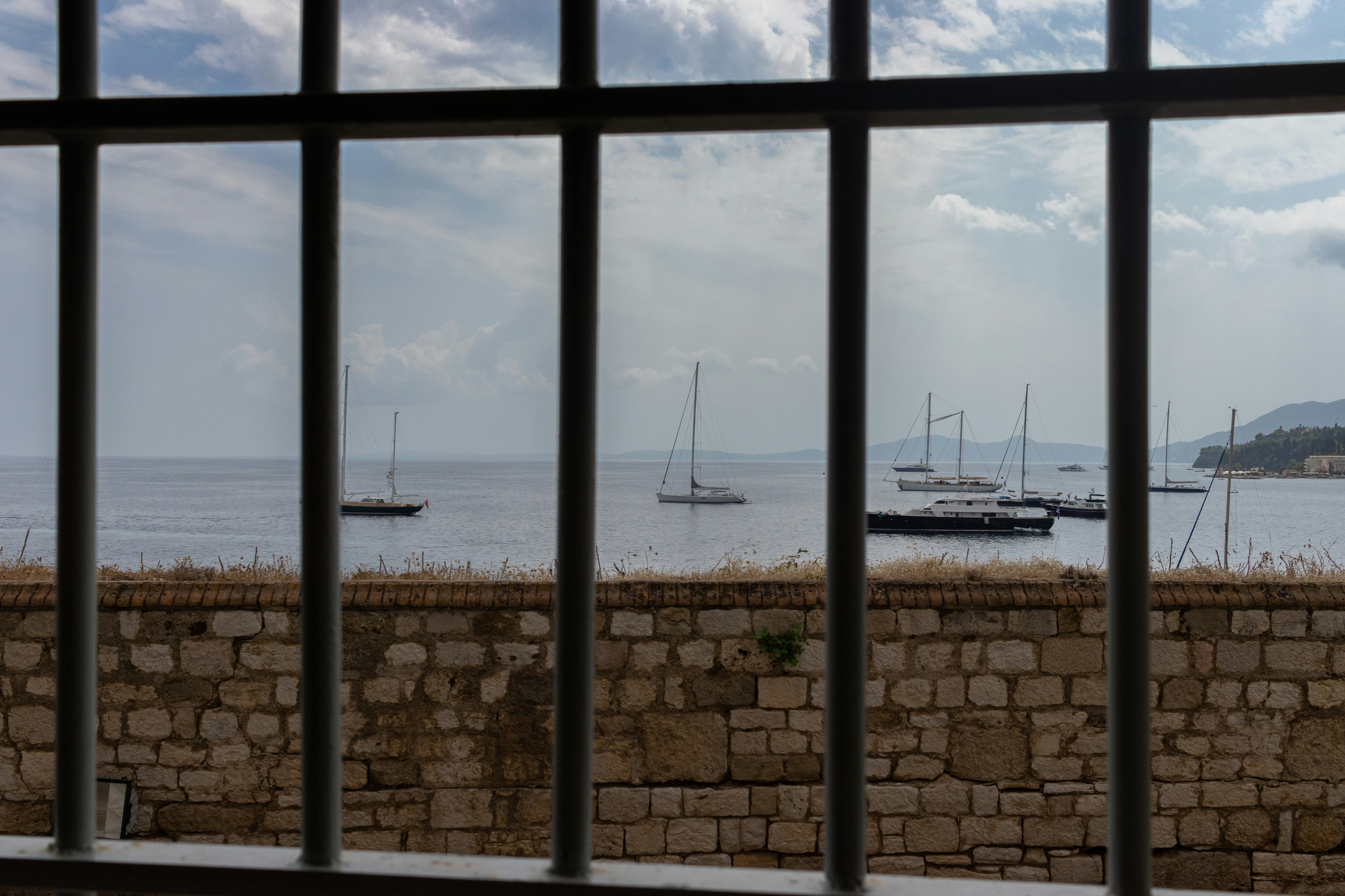Horizon Through Iron Rails: Sailboats Rest by a Weathered Stone Wall