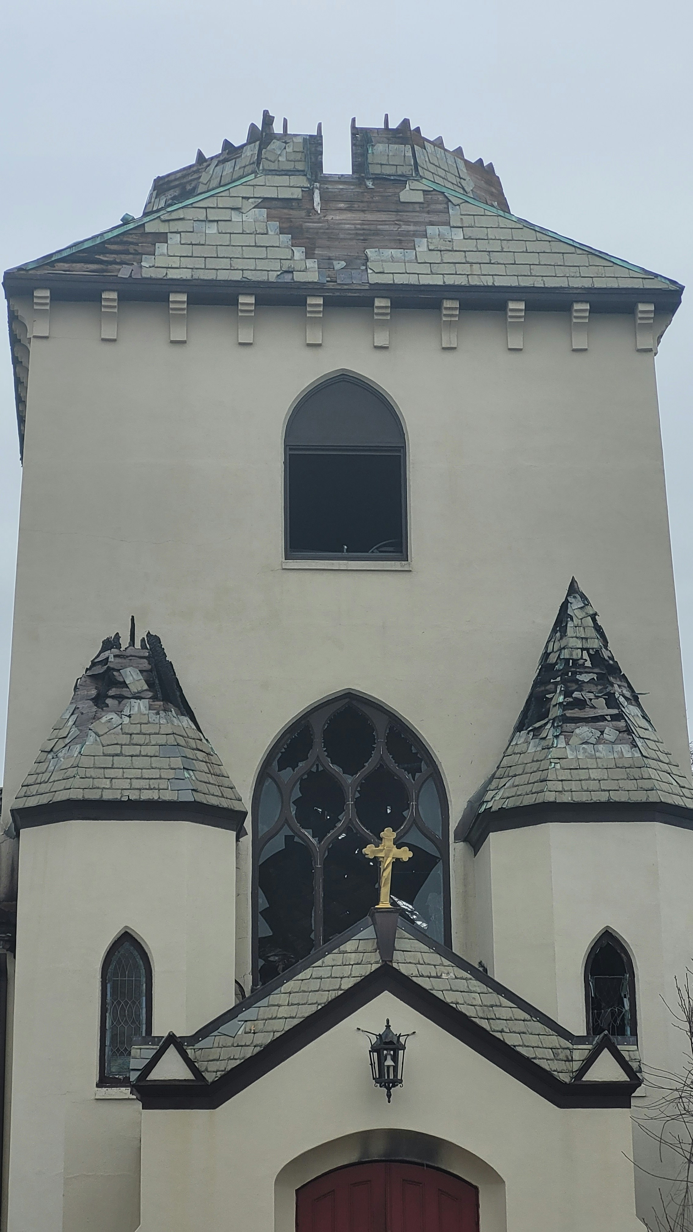Damaged church facade showcasing a broken roof and stained glass windows, with a prominent cross at the entrance.