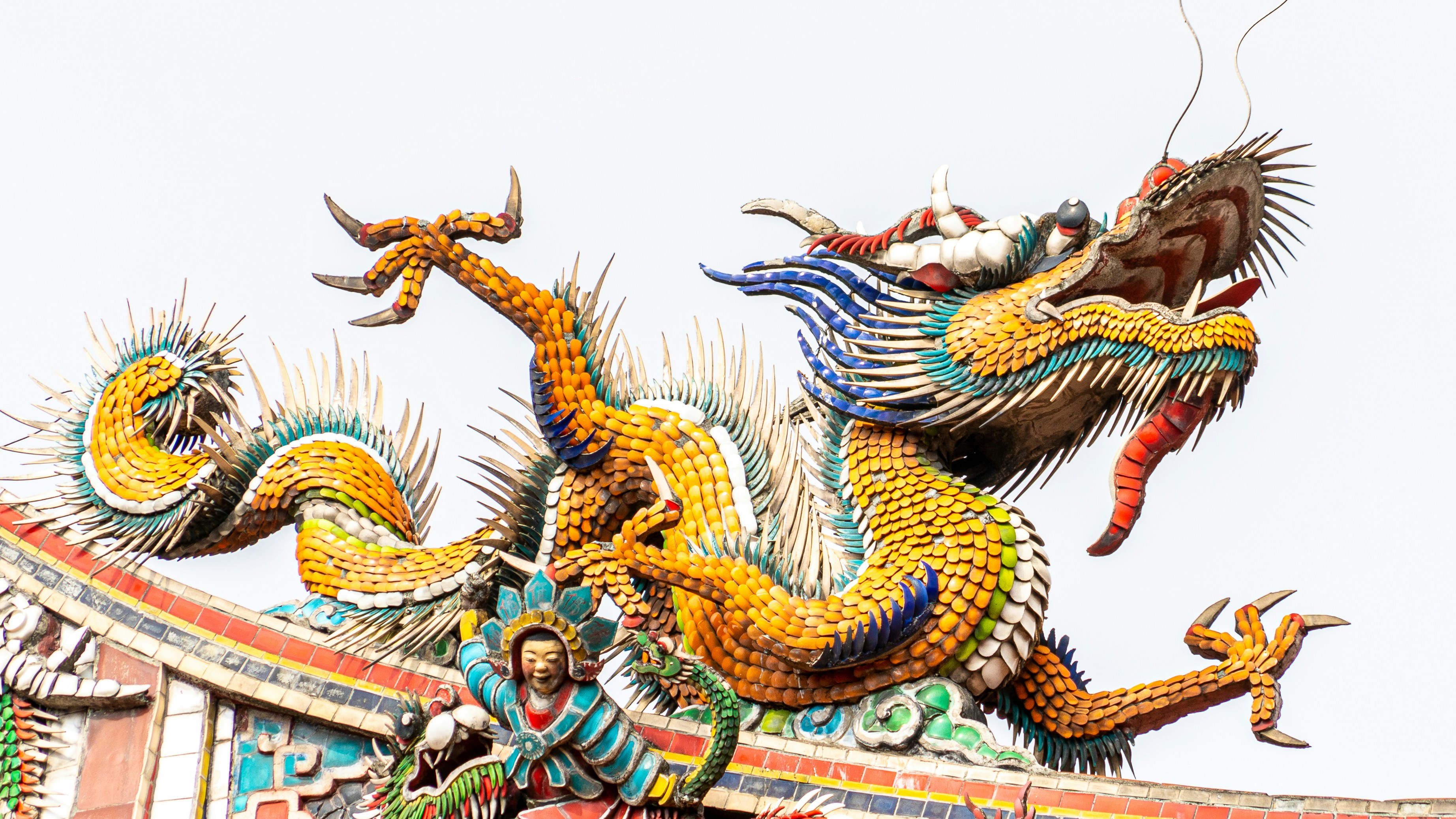 Vibrantly colored dragon sculpture perched atop a traditional temple roof, showcasing intricate details and craftsmanship.