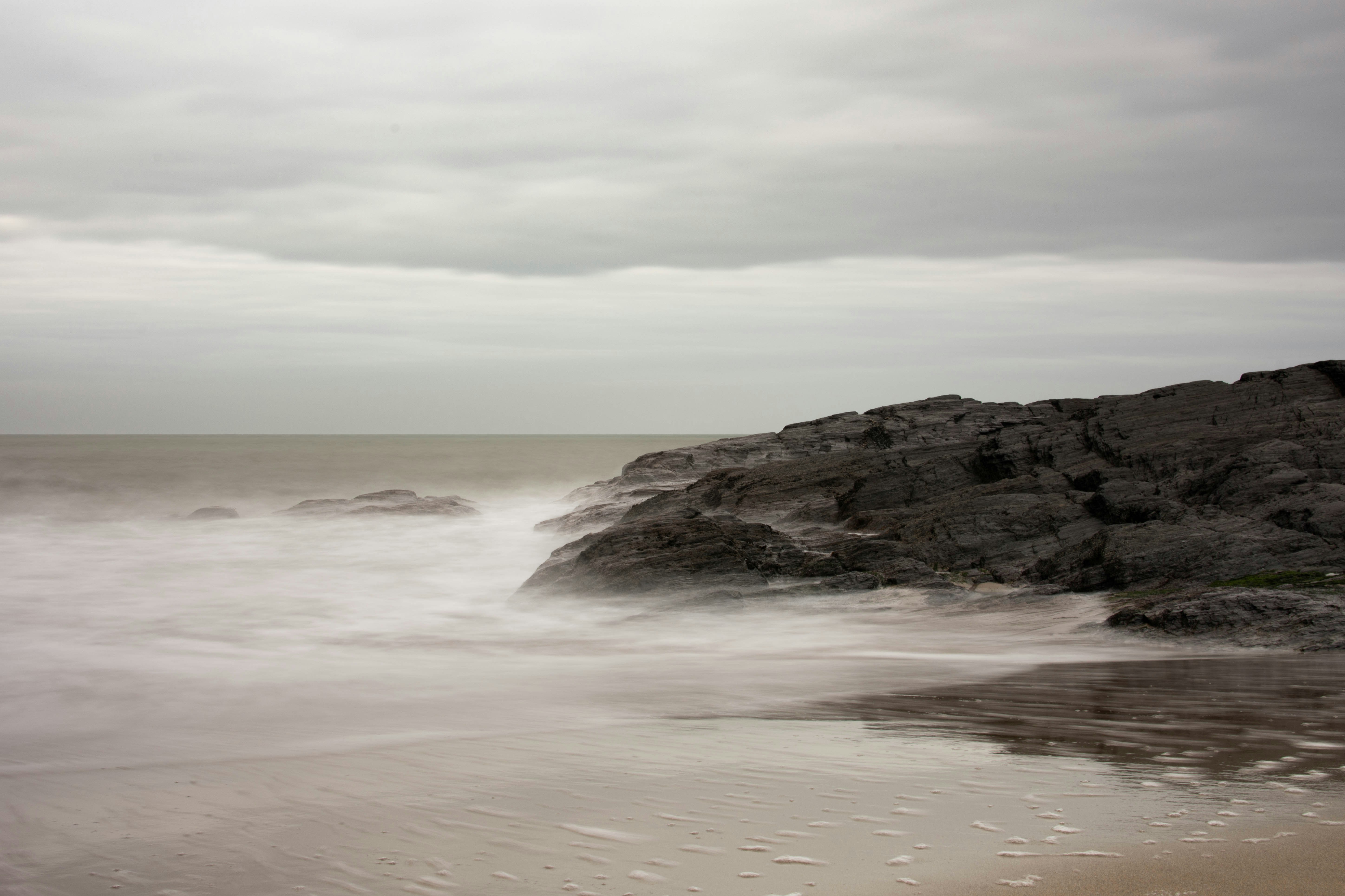 Long exposure on a winter ocean - waves crashing into rocks at a the beach of a hidden gem in Wales, United Kingdom. An overcast day with surprisingly calm seas, but still some rough waves to break over the rocks. | a rocky beach with waves coming in and out of the water