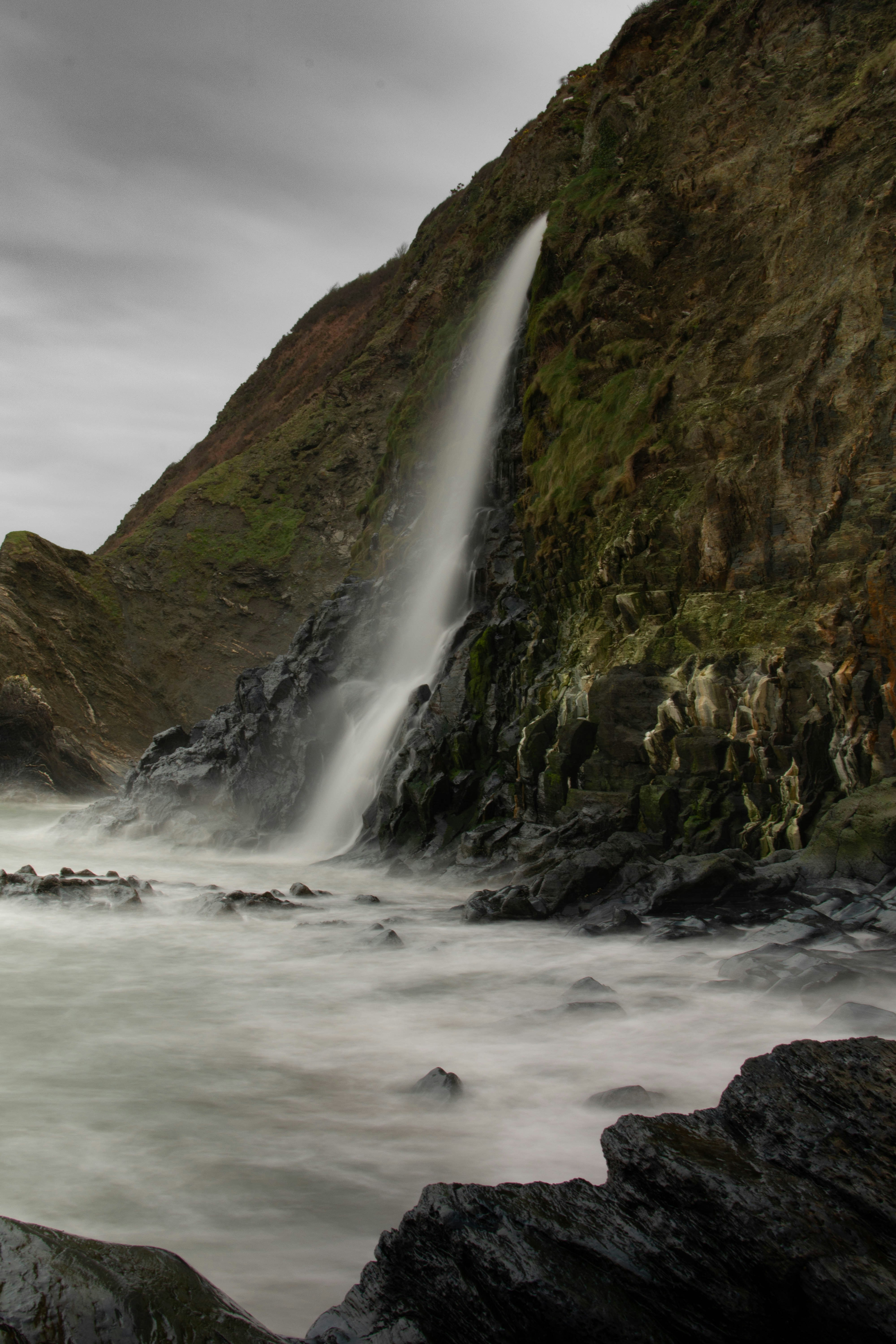 White Ribbon Cascading Off a Mossy Cliff into a Misty Seashore