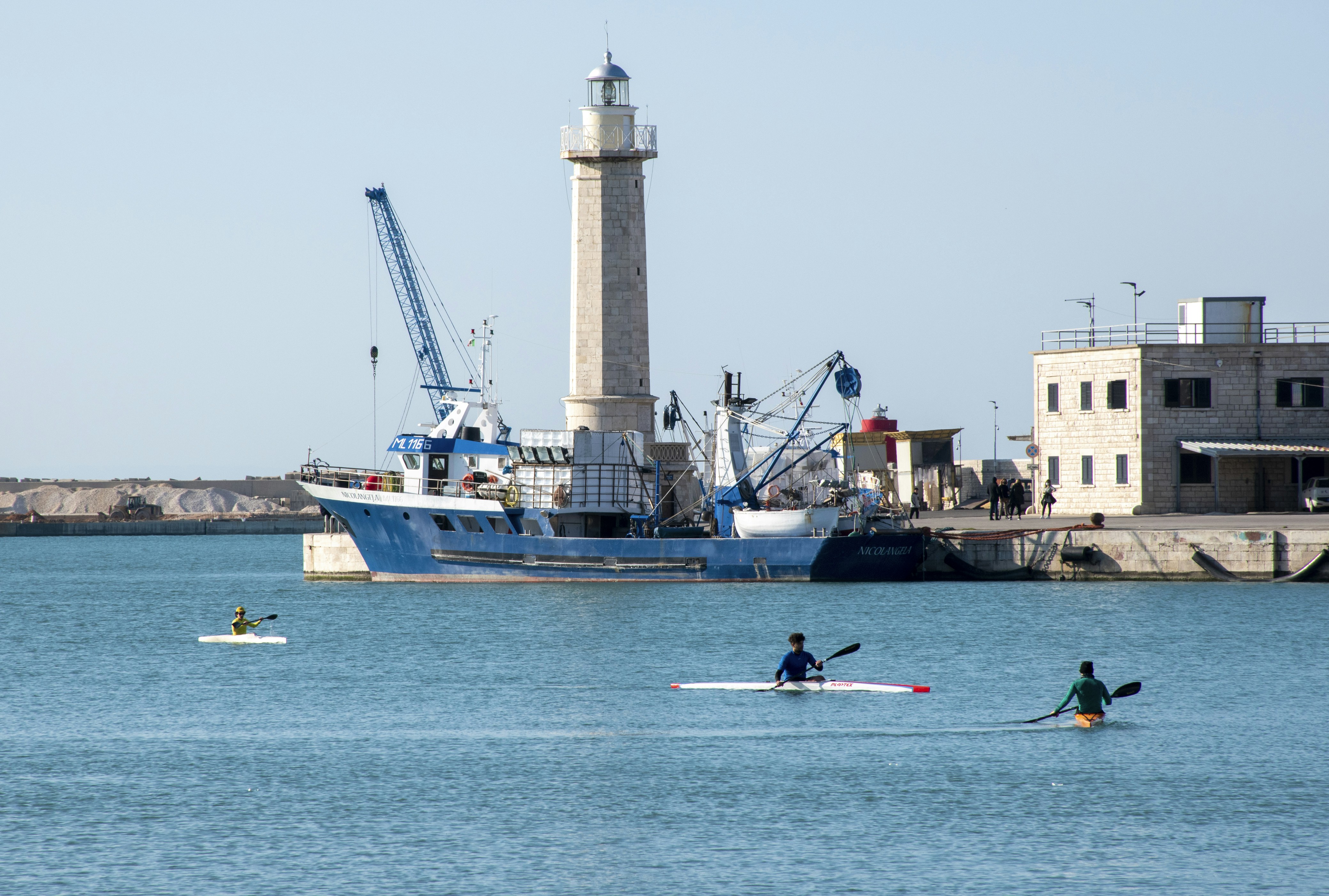 Kayakers glide through turquoise waters near a harbor lighthouse under a clear blue sky.