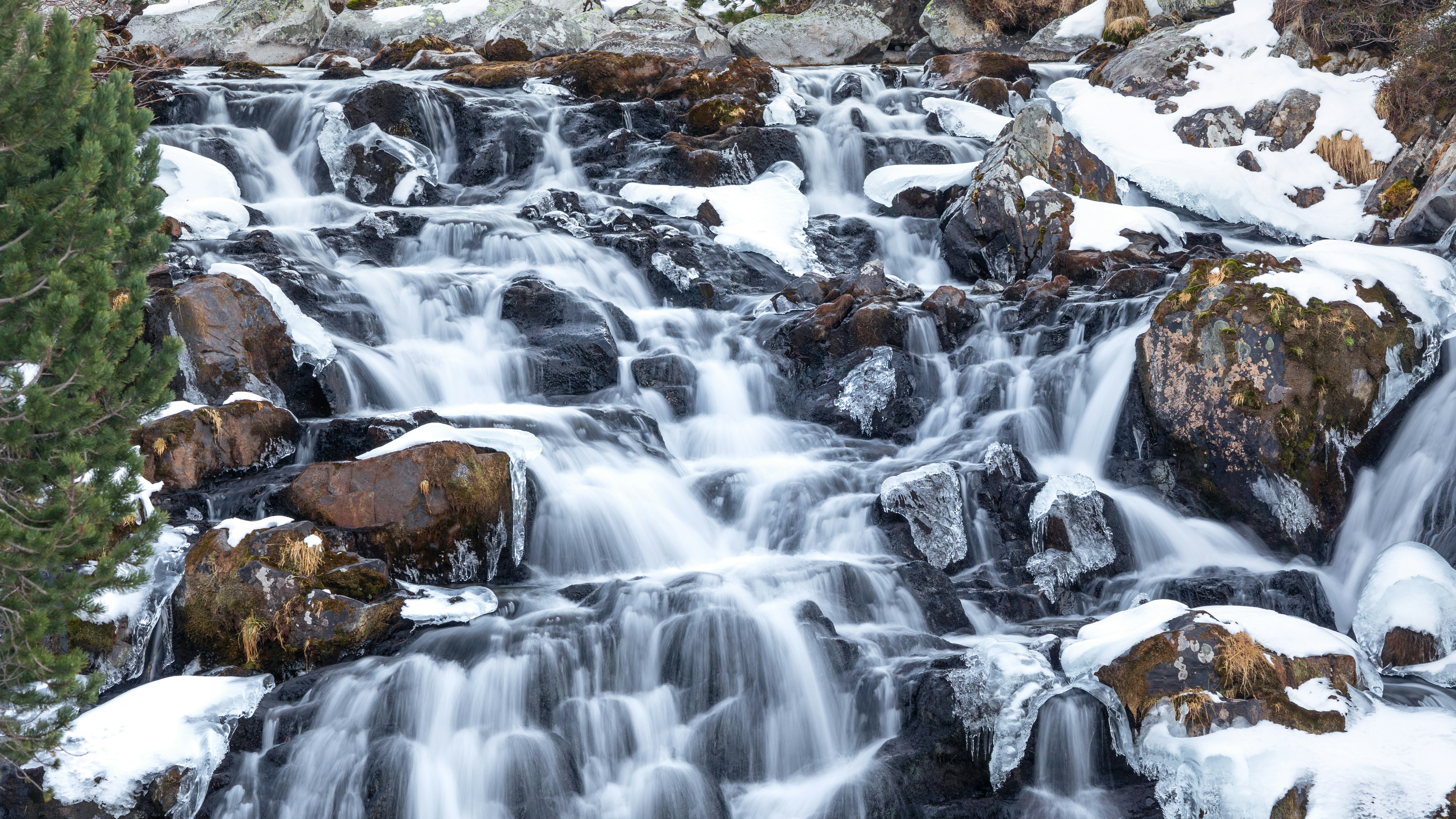 Snow-laden waterfall cascading over rocks in a serene, wintry landscape.