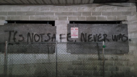 Caution Sign Centered on a Graffitied Wall, Framed by a Weathered Fence