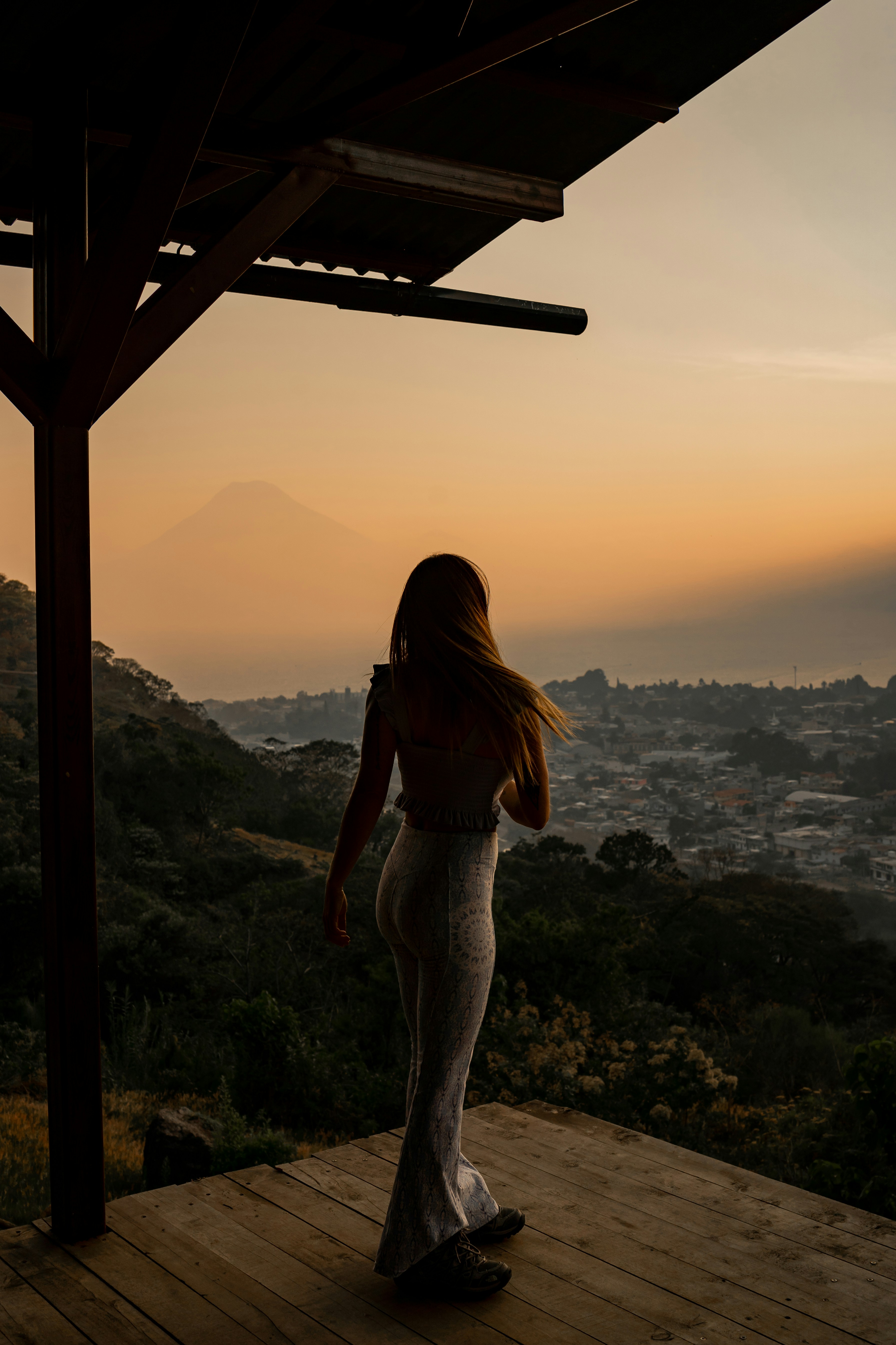 Terrace Silhouette at Dusk: A Figure Framed by Valley Lights and a Distant Volcano