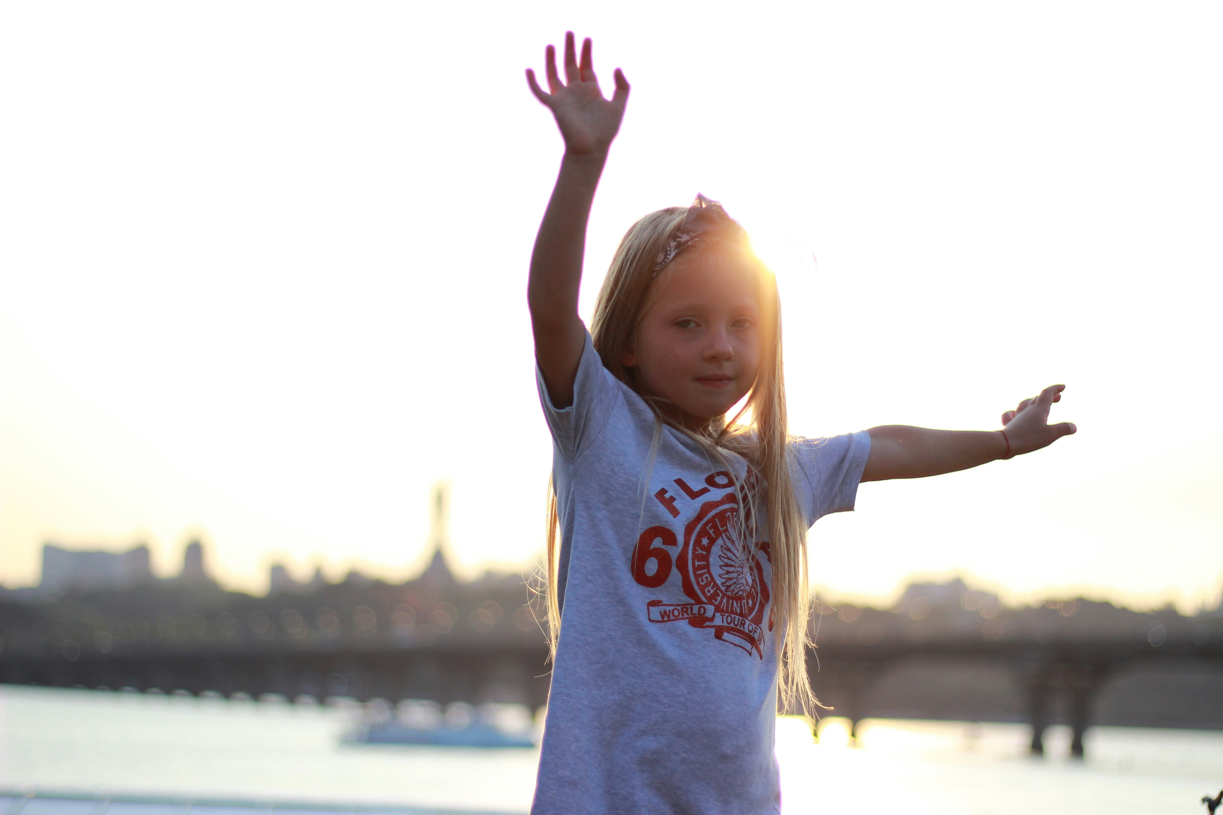 Sunlit Reach by the River: A Girl Waves Under Riverside Sunset