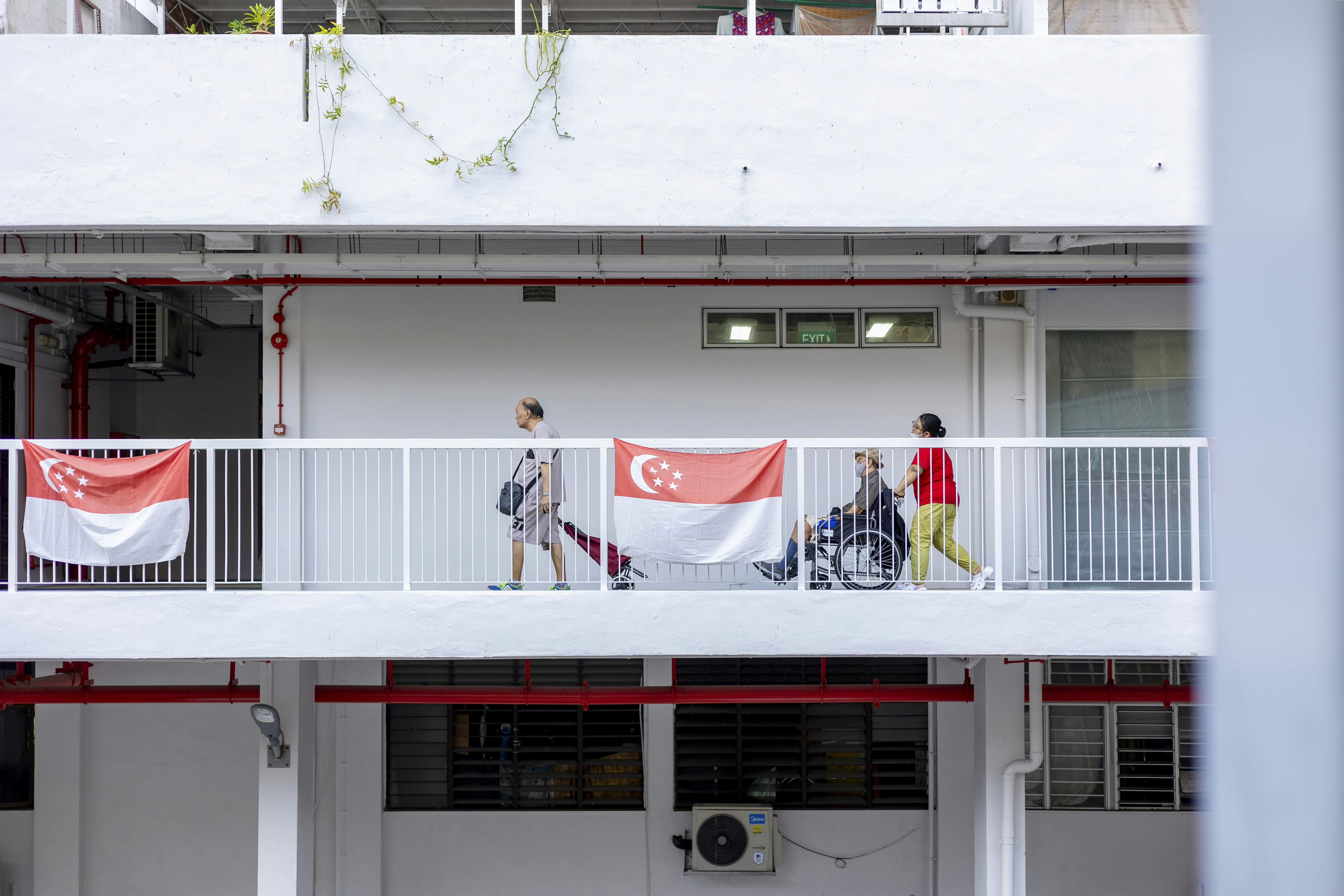 Residents stroll along a balcony adorned with Singapore flags, showcasing a blend of everyday life and national pride.