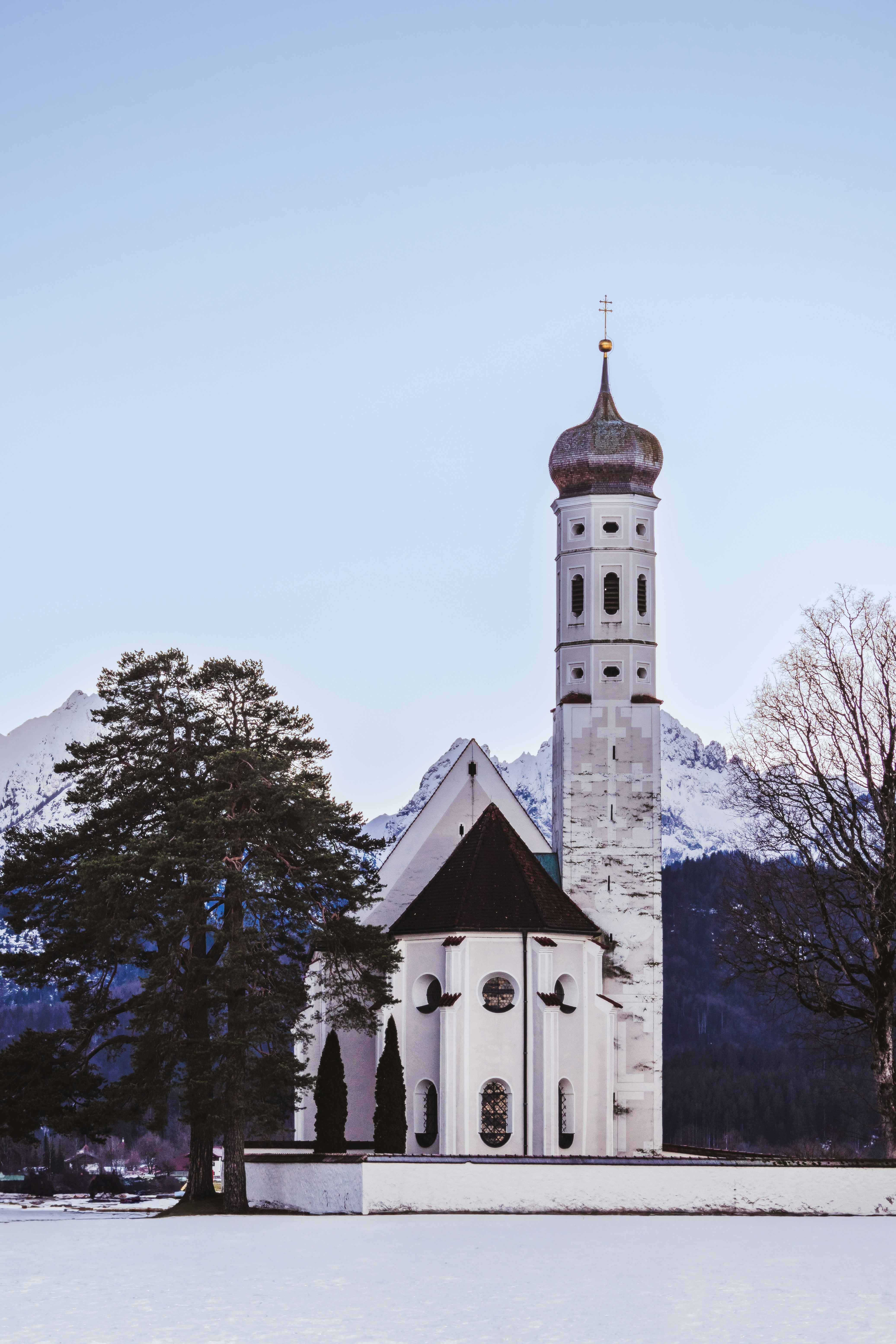 White Church Tower Rising Over Snowy Plain with Alpine Backdrop