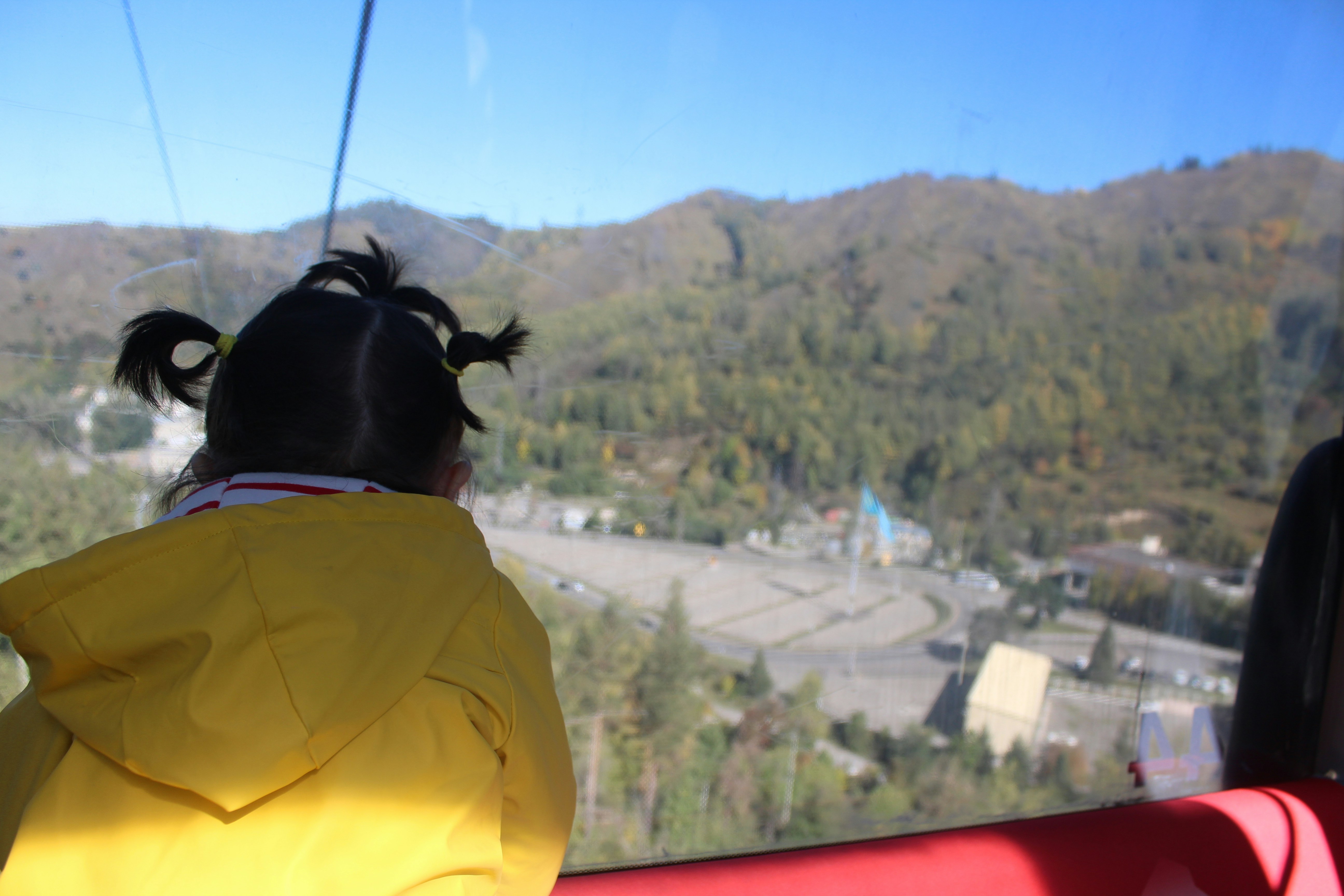 Bright Yellow Jacket in a Red Gondola: A Quiet Gaze Over the Alpine Valley