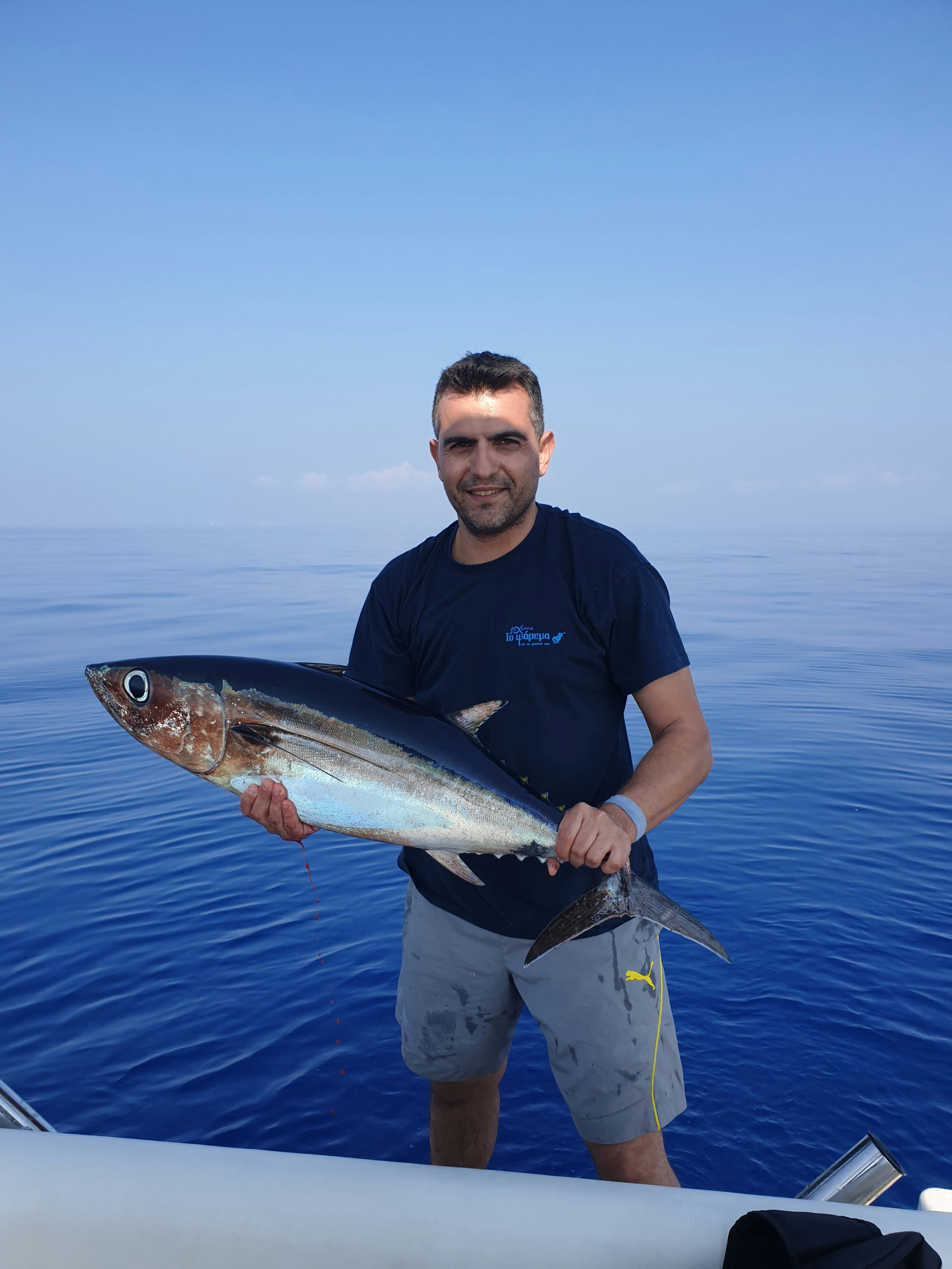 Bow-Side Prize: A man with a gleaming sea catch against a glassy blue ocean