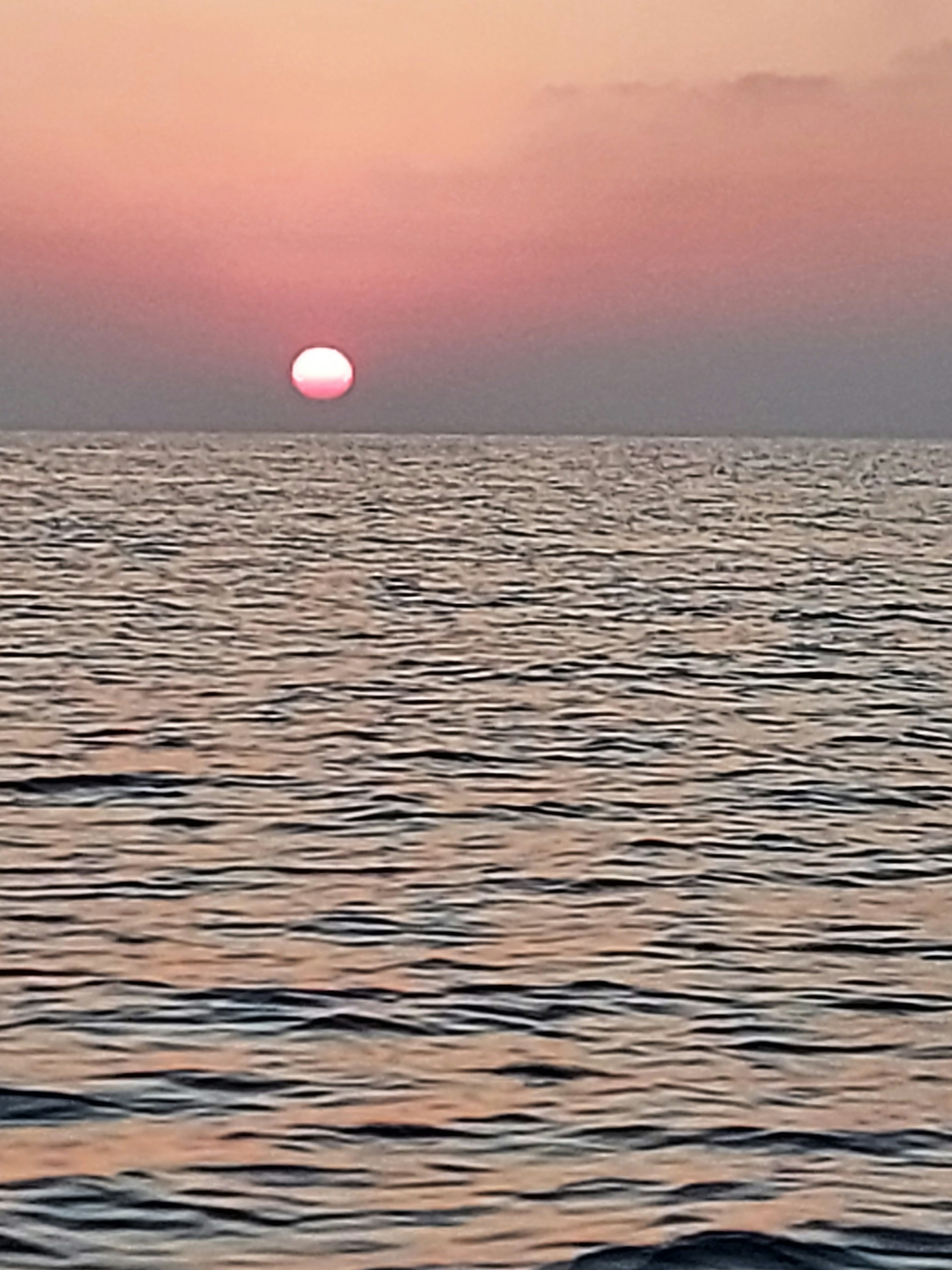 Sunset over a calm sea with a pink-hued sky meeting the water at the horizon.