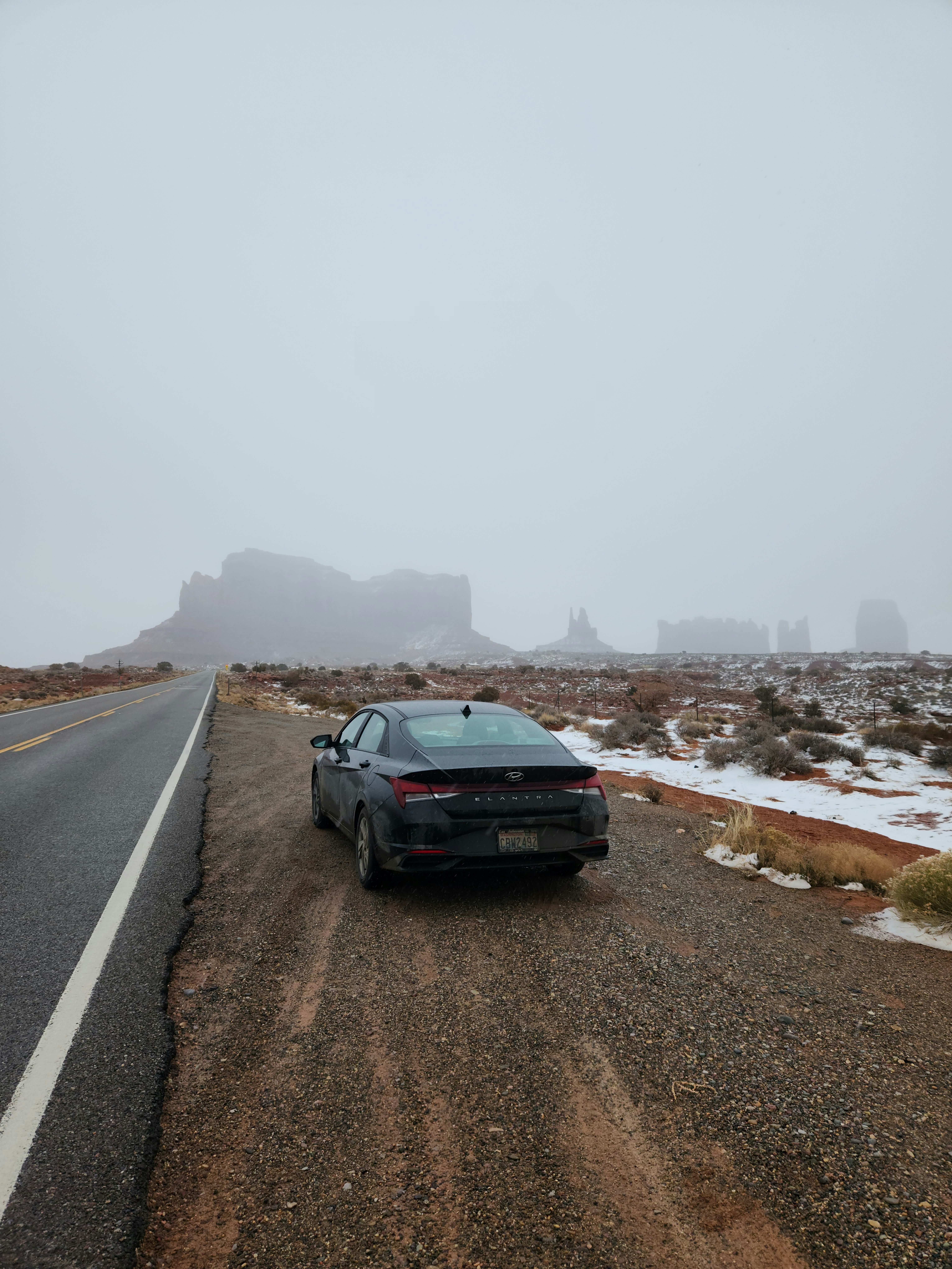 Mist-Blanketed Desert: A Sedan Pauses at the Edge of Buttes