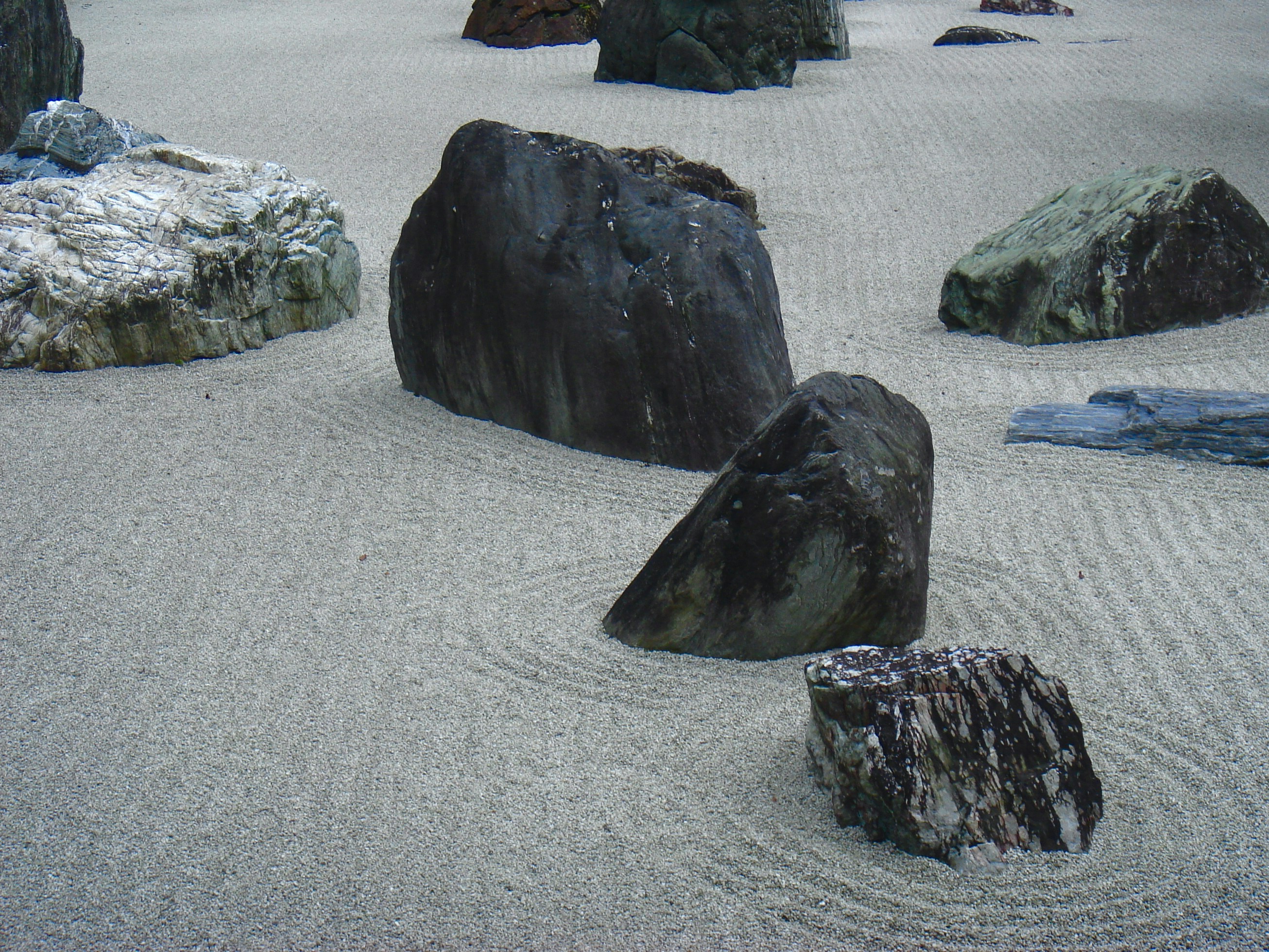 A collection of textured rocks scattered across a sandy beach, with gentle ripples in the sand creating a tranquil atmosphere.