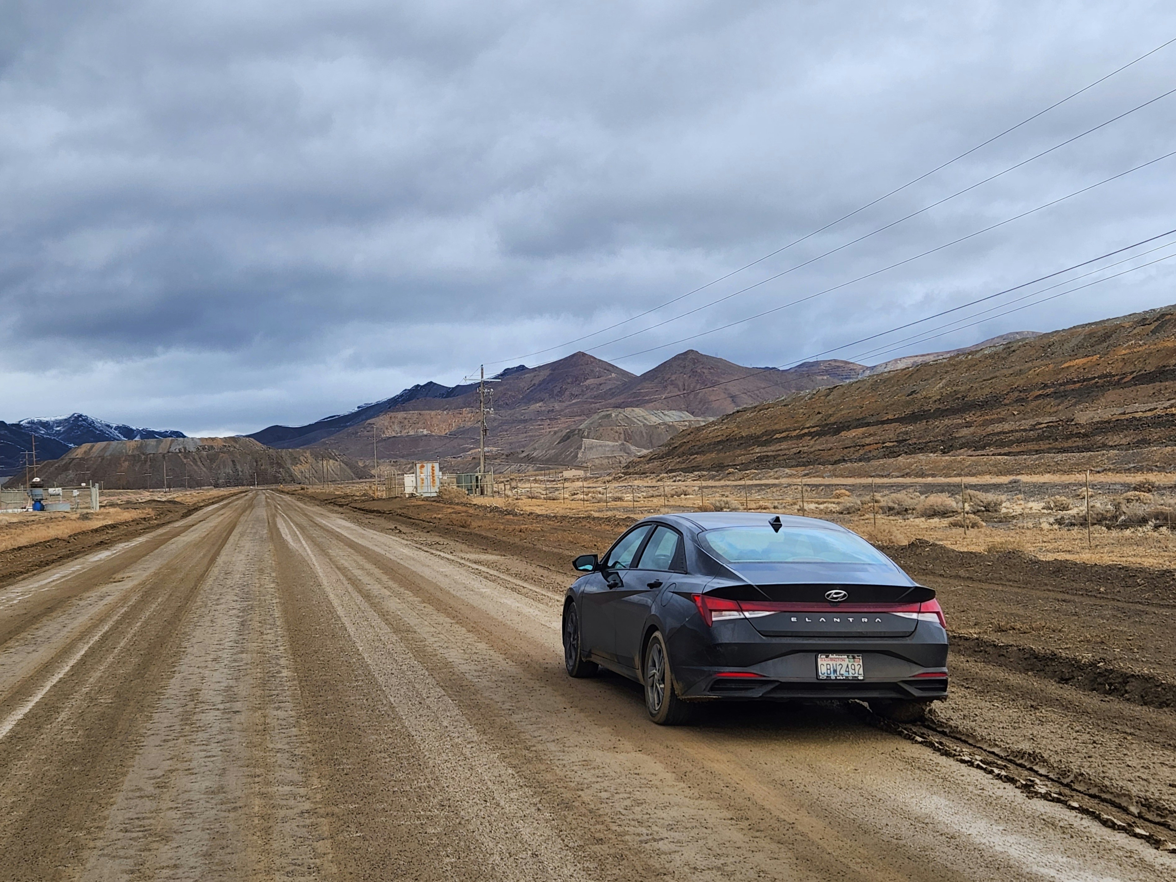Car parked on a muddy road leading to distant mountains under a cloudy sky.