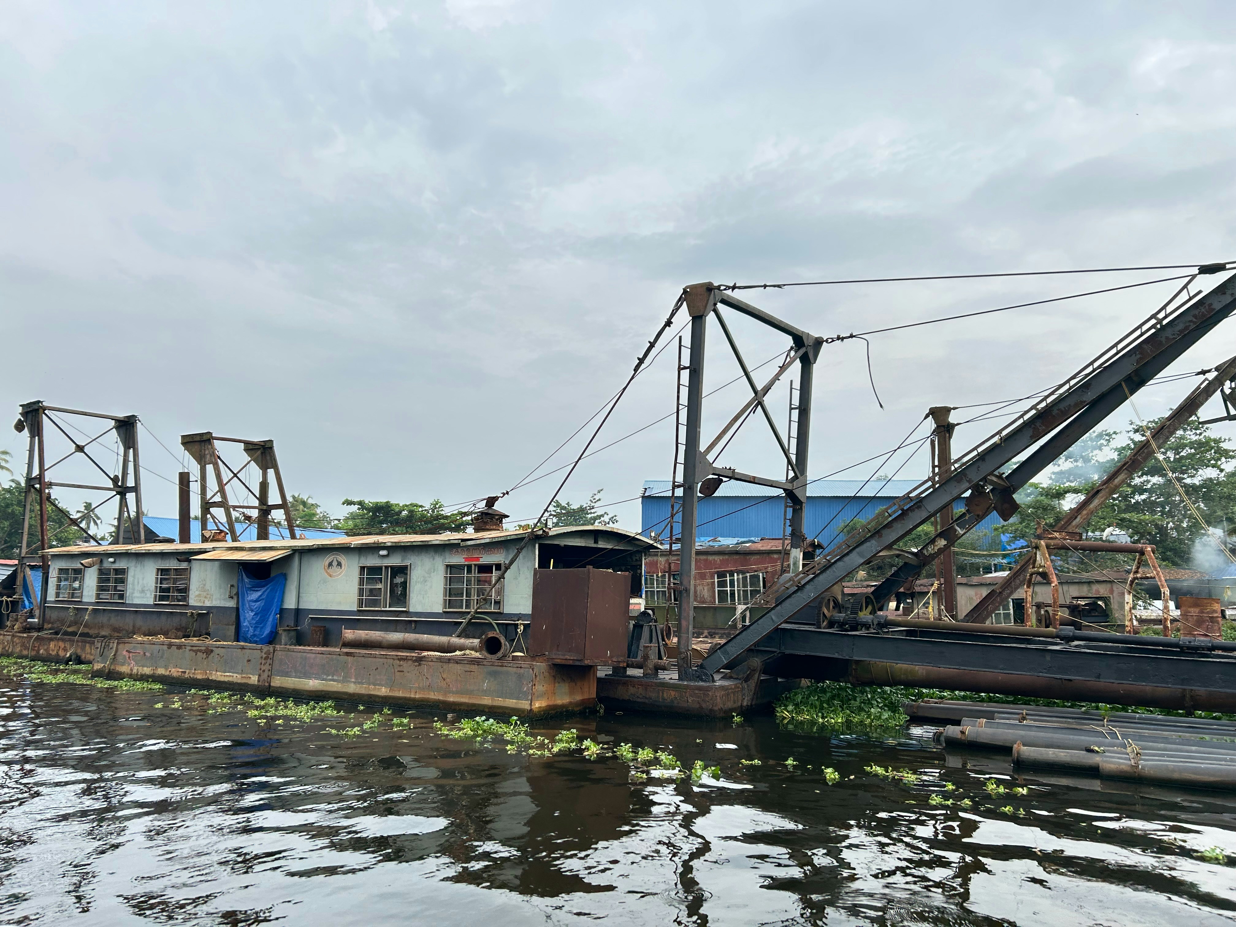 Industrial barge anchored on a calm river under a cloudy sky.