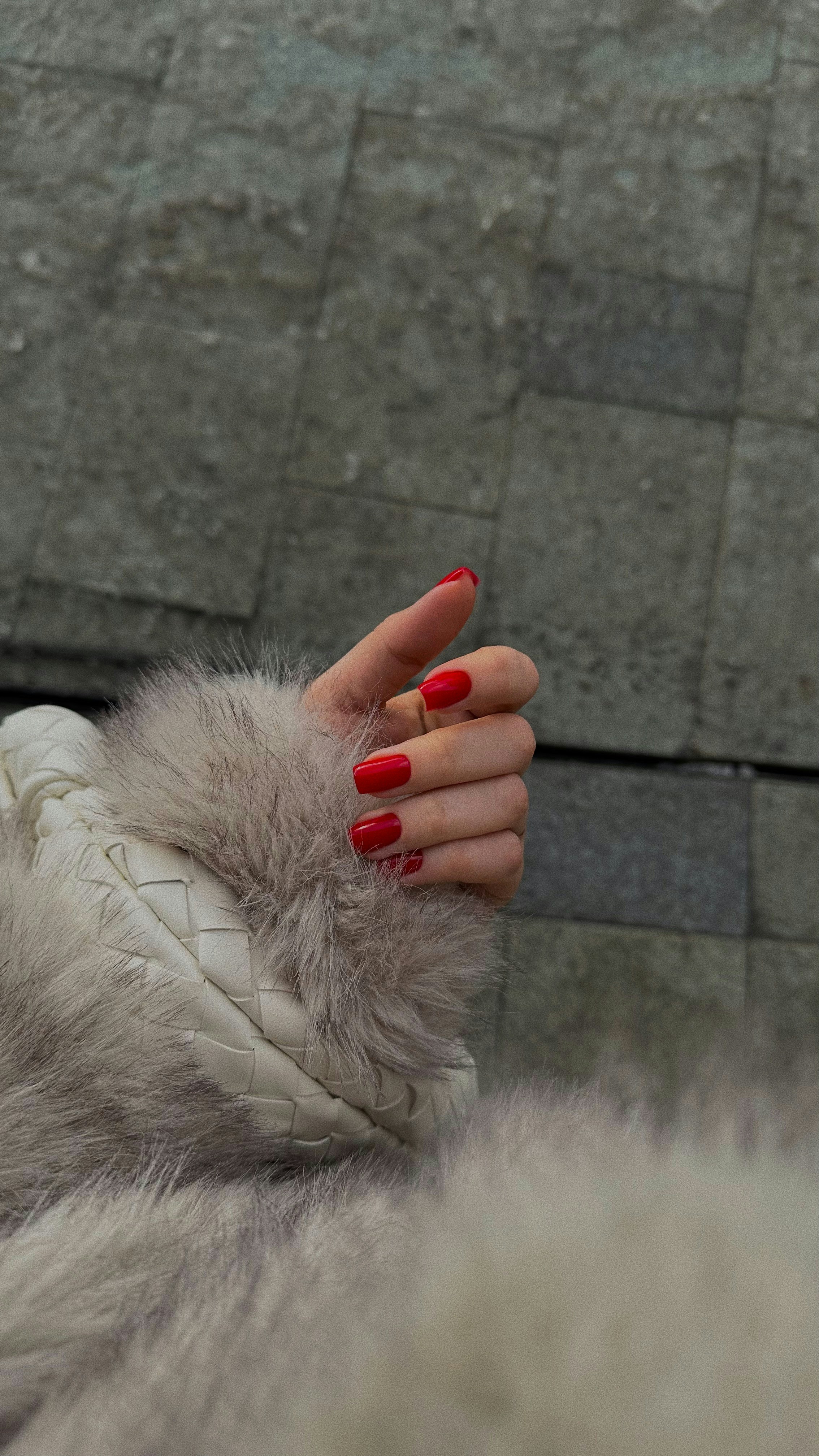Crimson Nails Clasp a Fluffy Fur with a Woven Clutch Against Stone