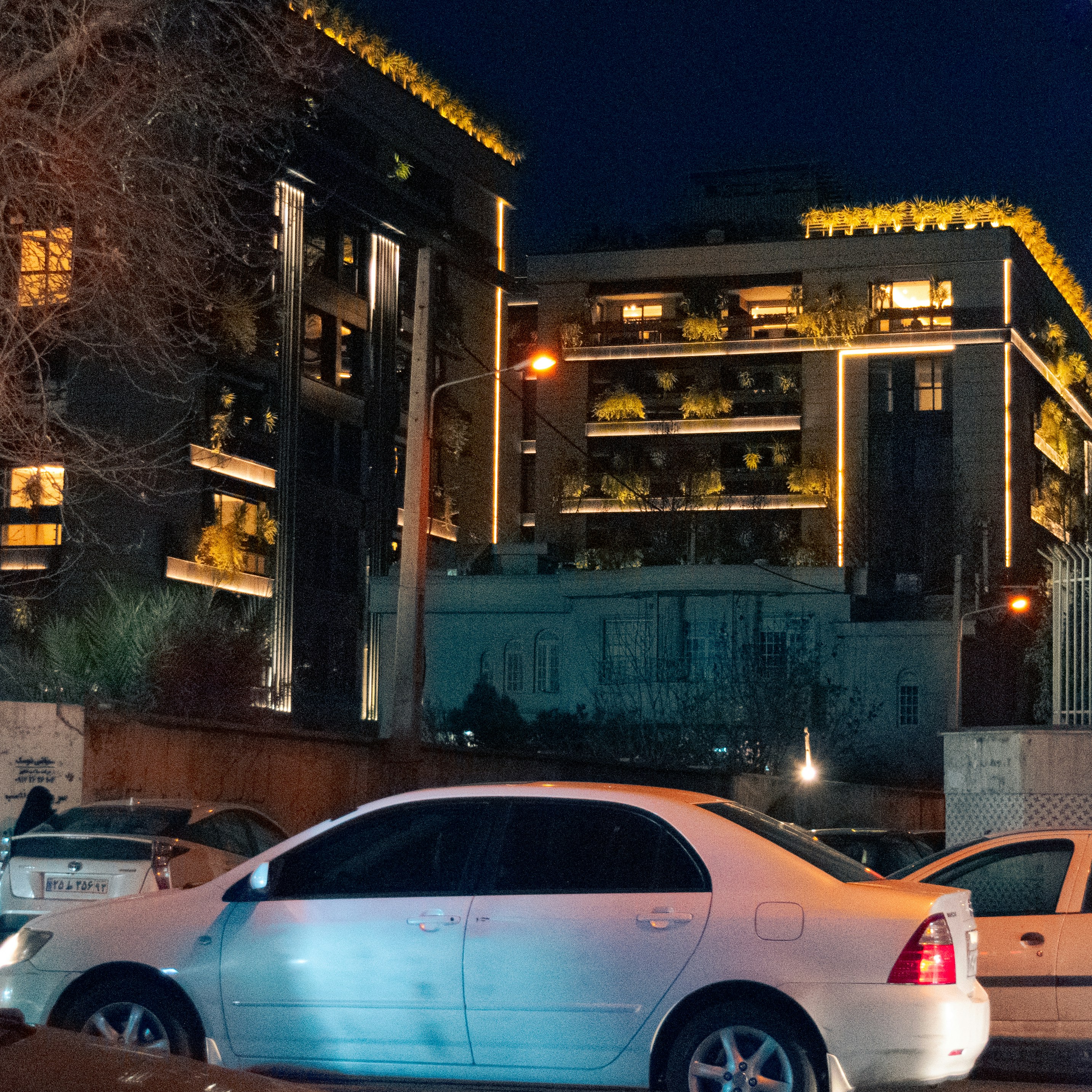 Midnight Glide: A Silver Sedan Beneath Amber-Illuminated Modern Towers