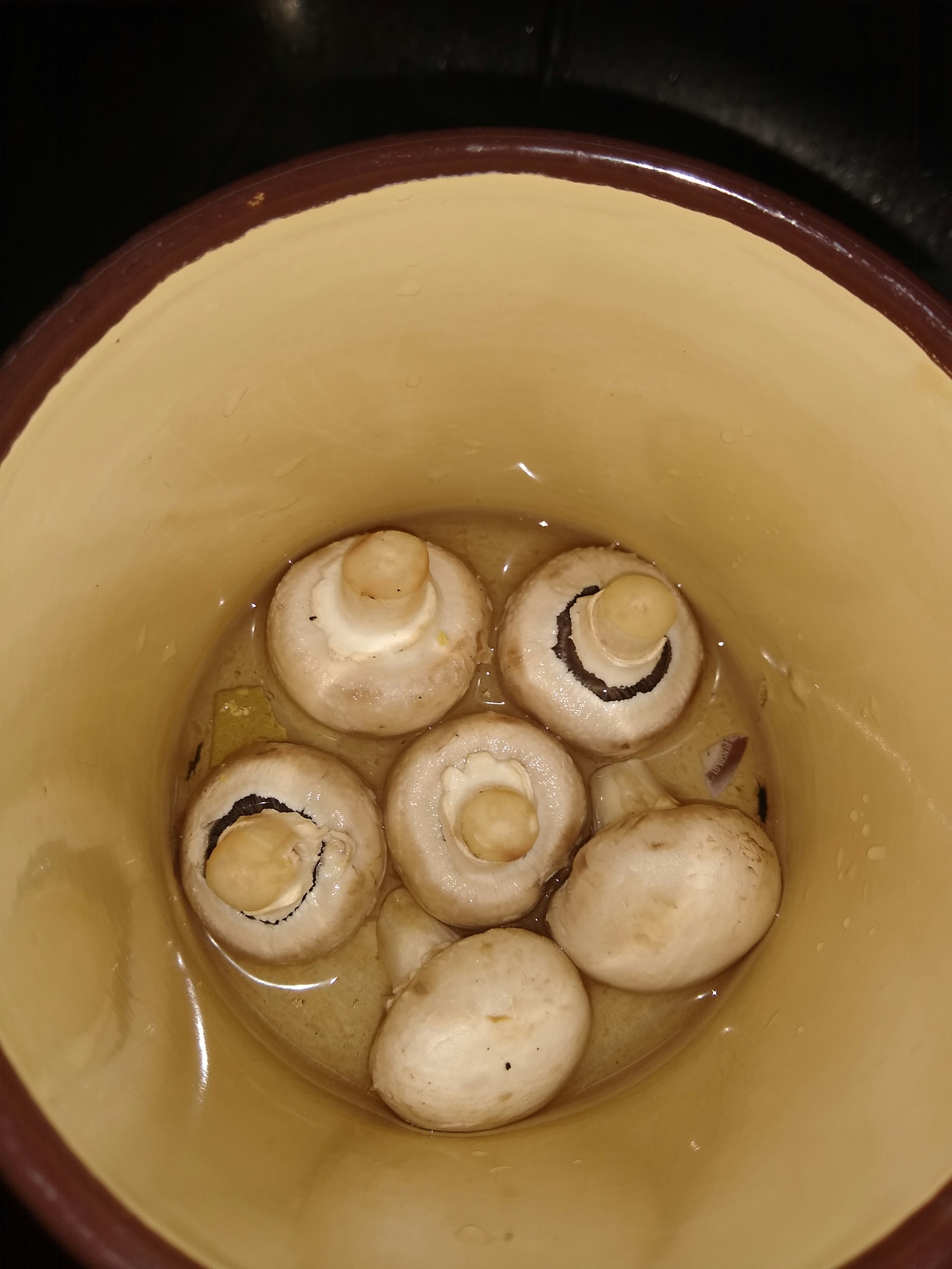 Close-up photograph of a beige ceramic cup holding a cluster of white button mushrooms, bathed in warm indoor light. The image highlights texture and scale in a tiny, quiet scene.