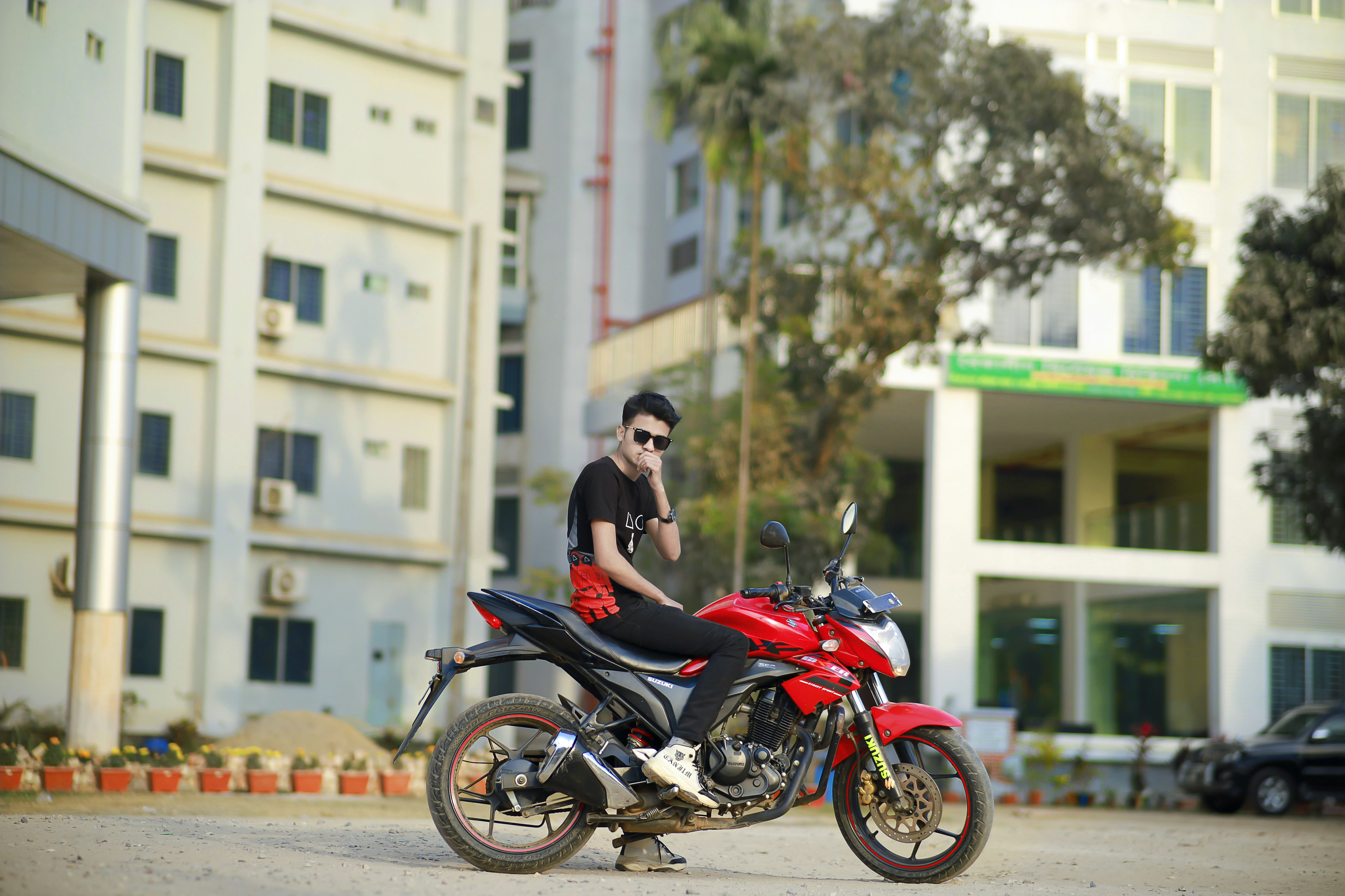 Sunlit Pause: A Rider Reposes on a Red Motorcycle Amid Quiet Campus Buildings