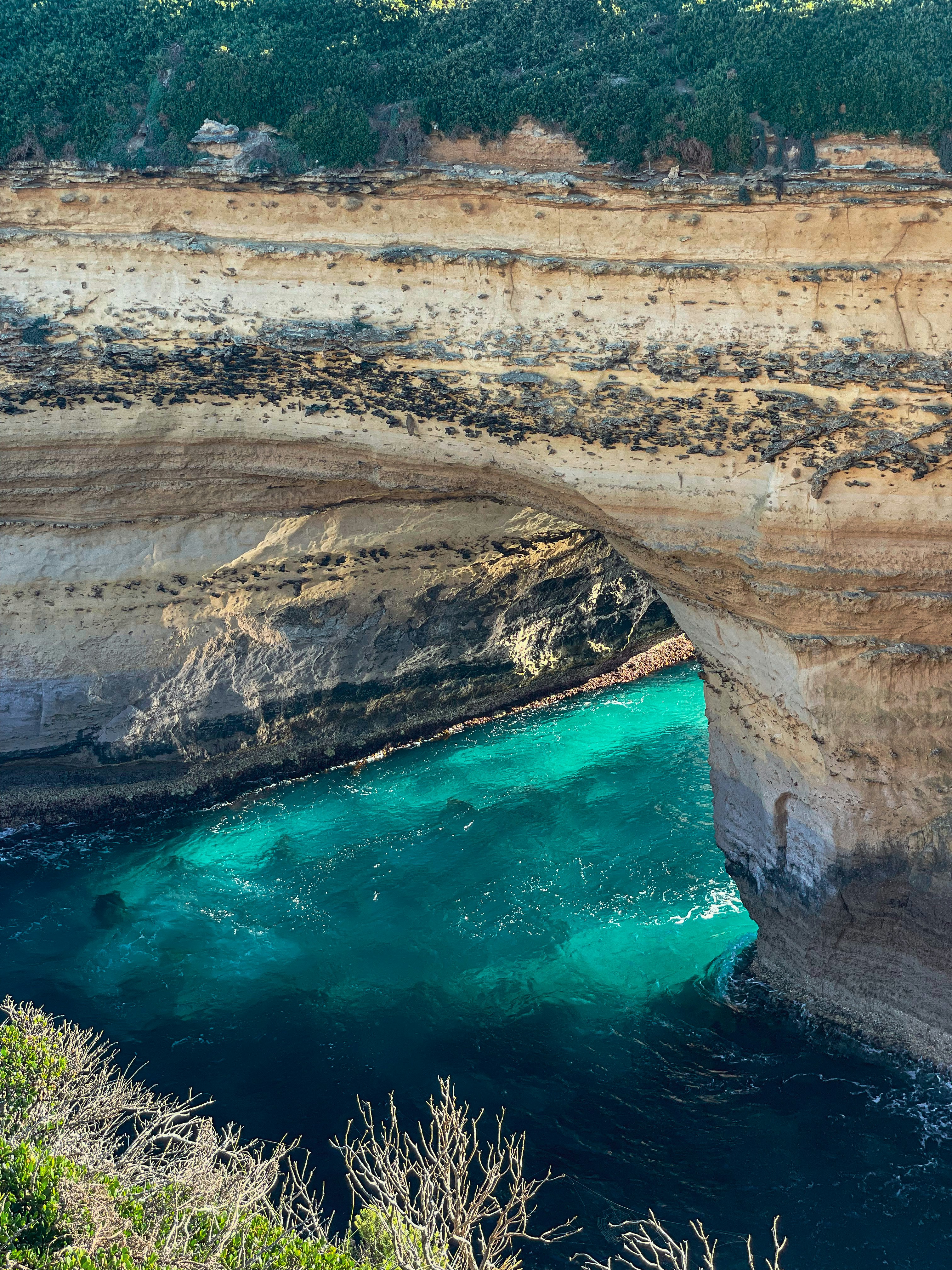 Turquoise waters glisten beneath a natural stone arch, surrounded by rugged cliffs and lush vegetation.