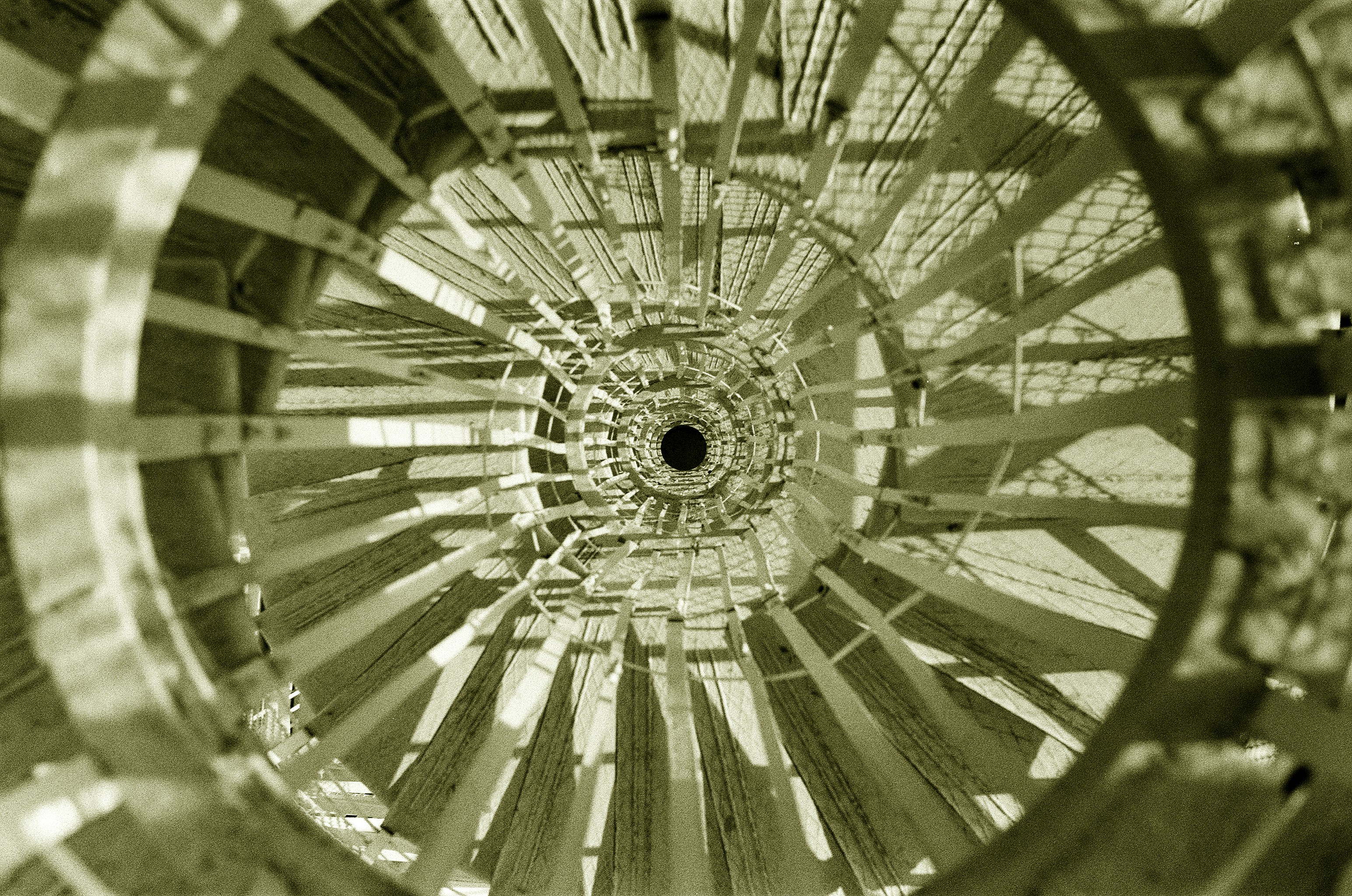 Intricate circular staircase viewed from above, casting geometric shadows in sepia tones.