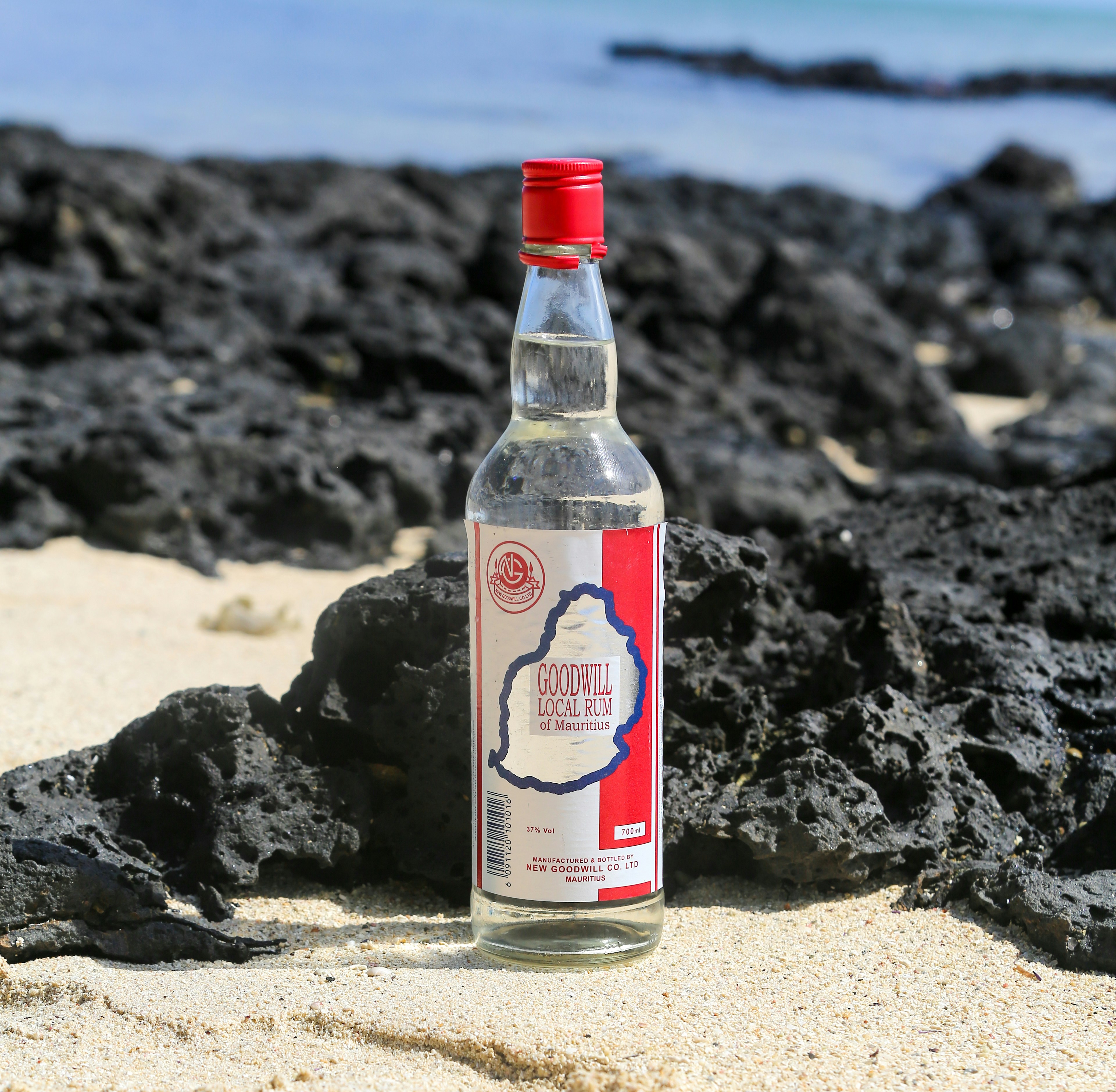 Crimson Cap on Lava Beach: A bottle standing amid black rocks and sunlit sand