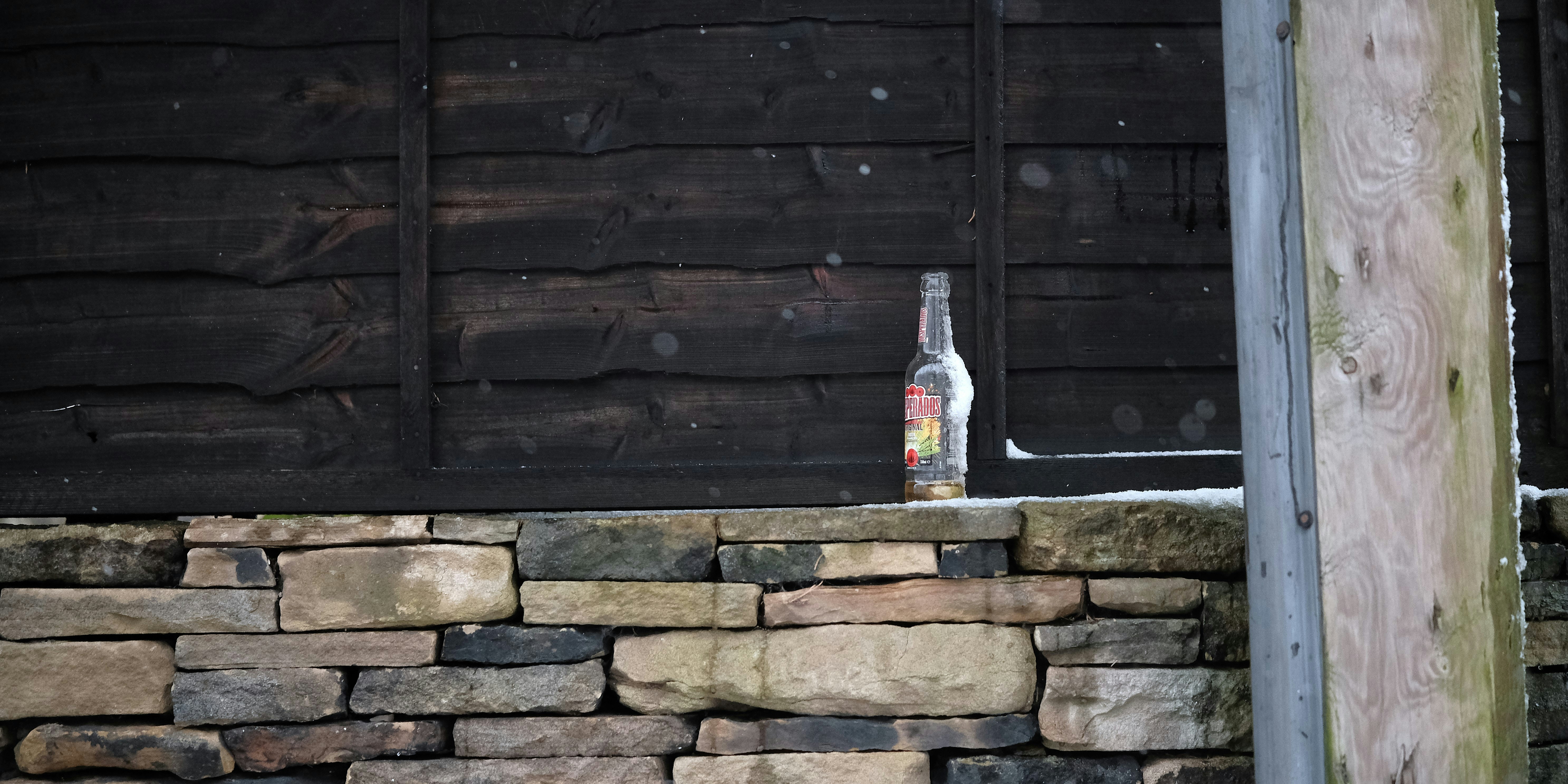 Disused beer bottle on a weathered ledge against a dark wooden wall
