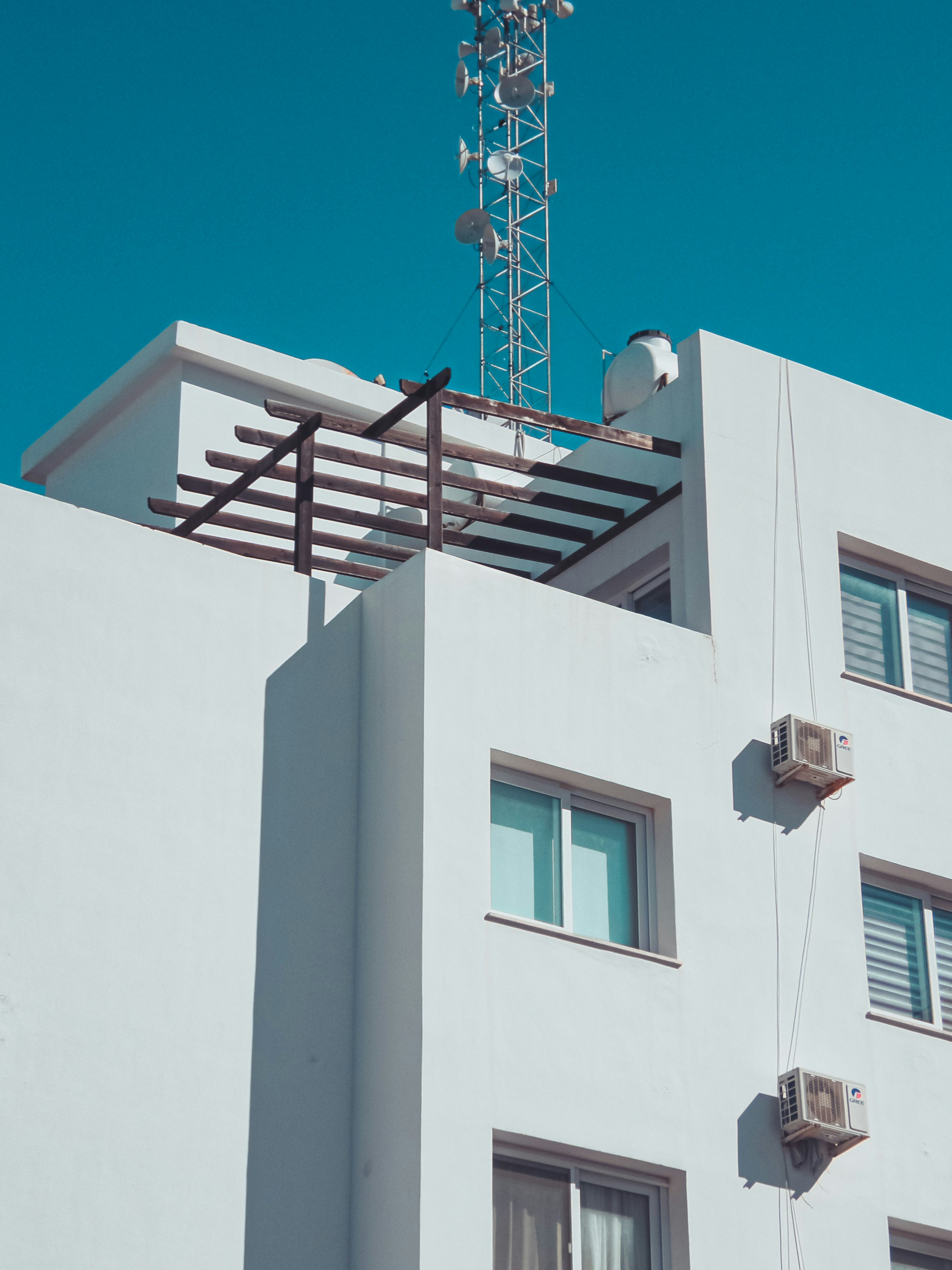 Clean architectural detail of a white building rooftop with antenna array and exposed HVAC units; a modernist composition emphasizing geometric planes and shadows.