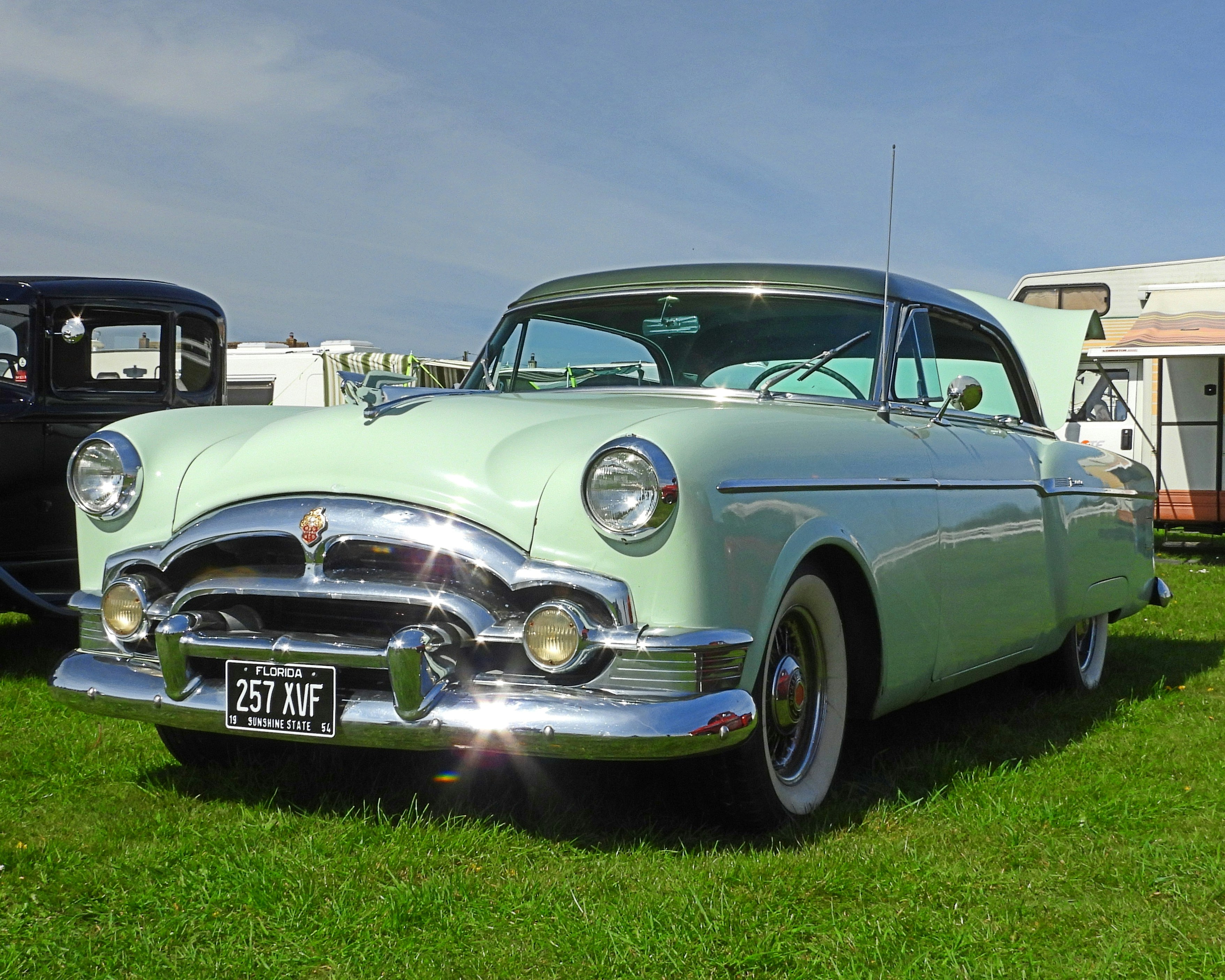 Classic pastel green car parked on grassy field, showcasing its vintage design and chrome accents.