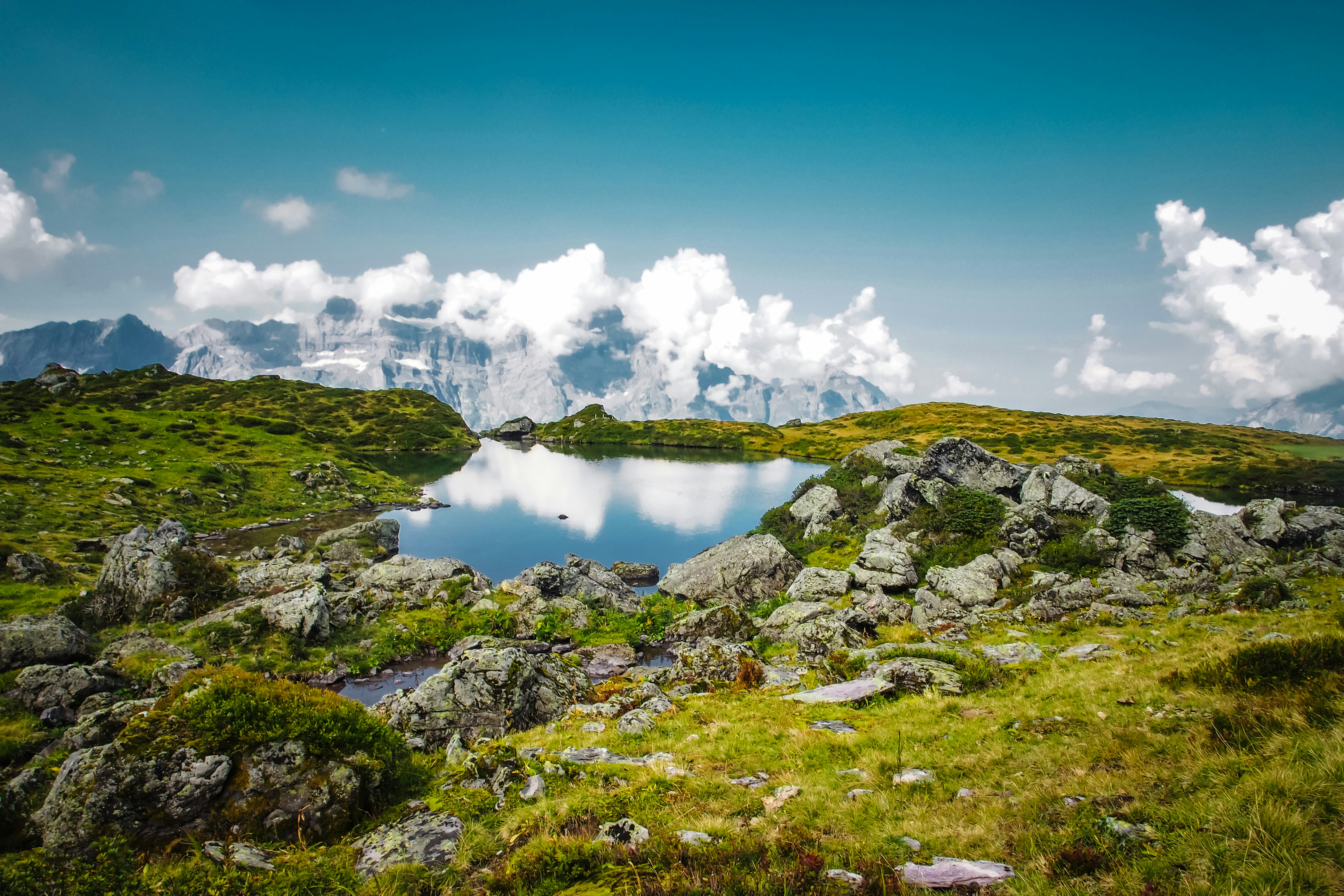 A mountain lake surrounded by rocks and grass photo – Free Lake Image ...