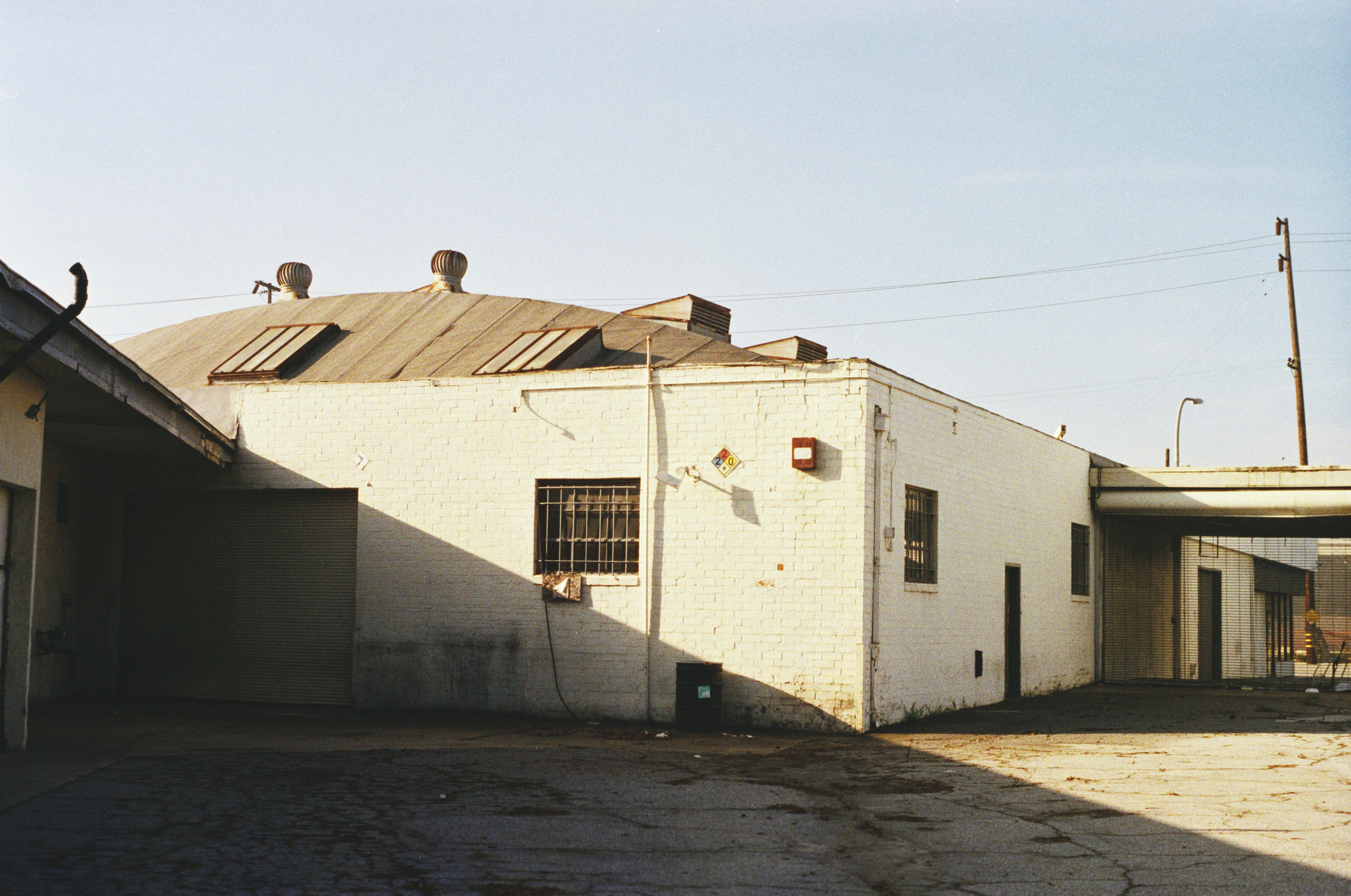 White building with a metal roof casting long shadows beside a sunlit parking lot.