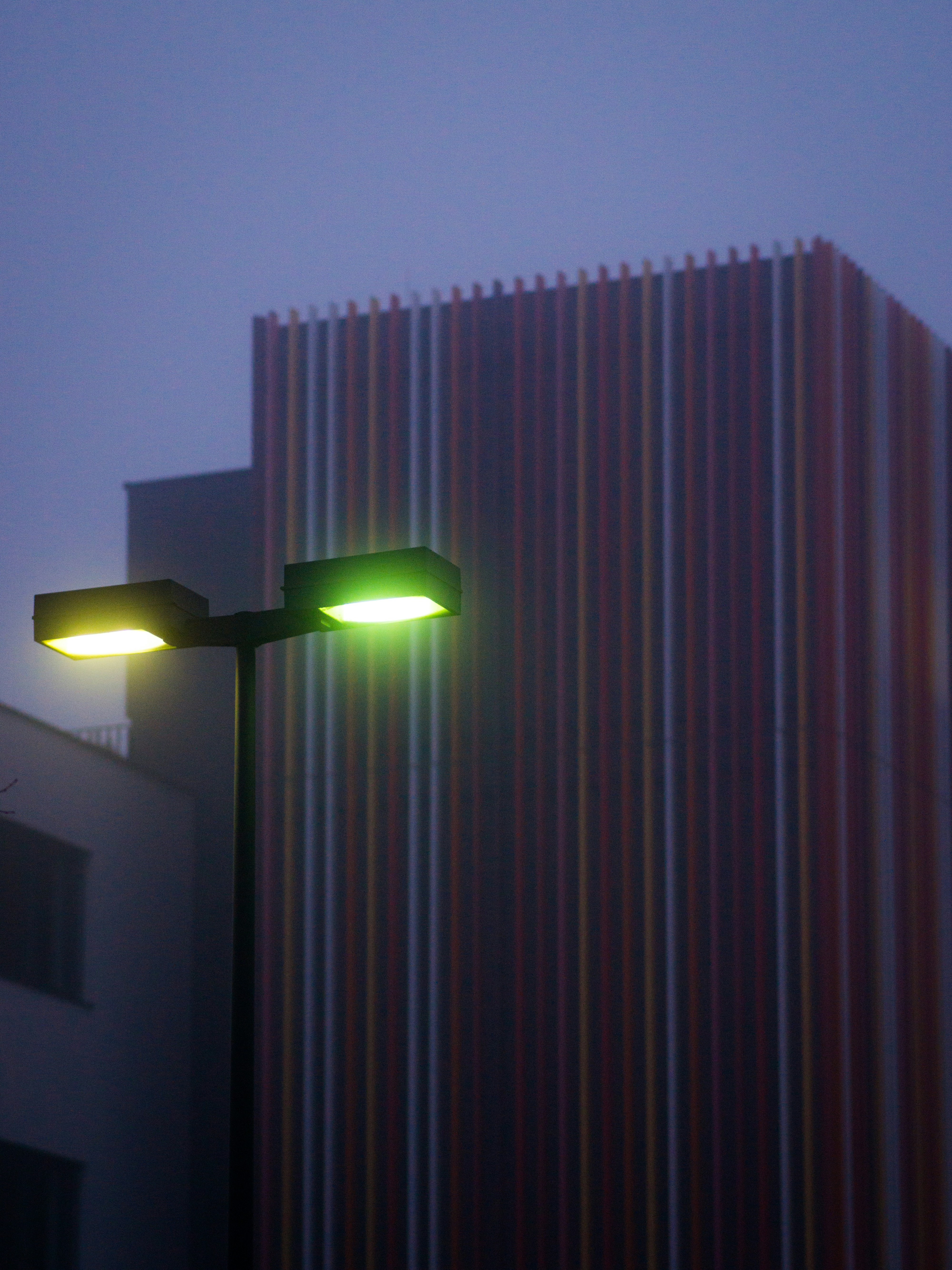 Green-lit Streetlamp Against a Striated Facade at Dusk