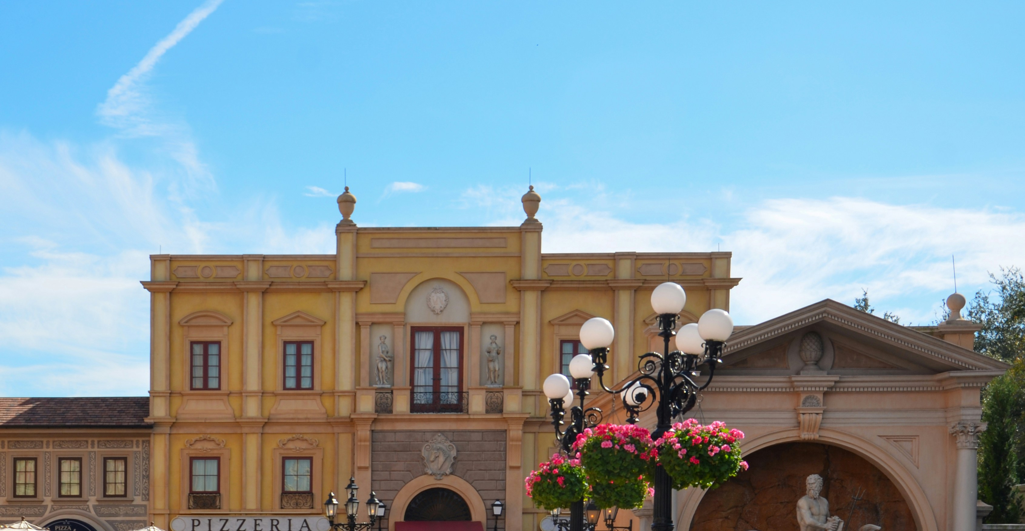 Ornate Mediterranean-style building with arched windows and a lamppost adorned with pink flowers, set against a bright blue sky.