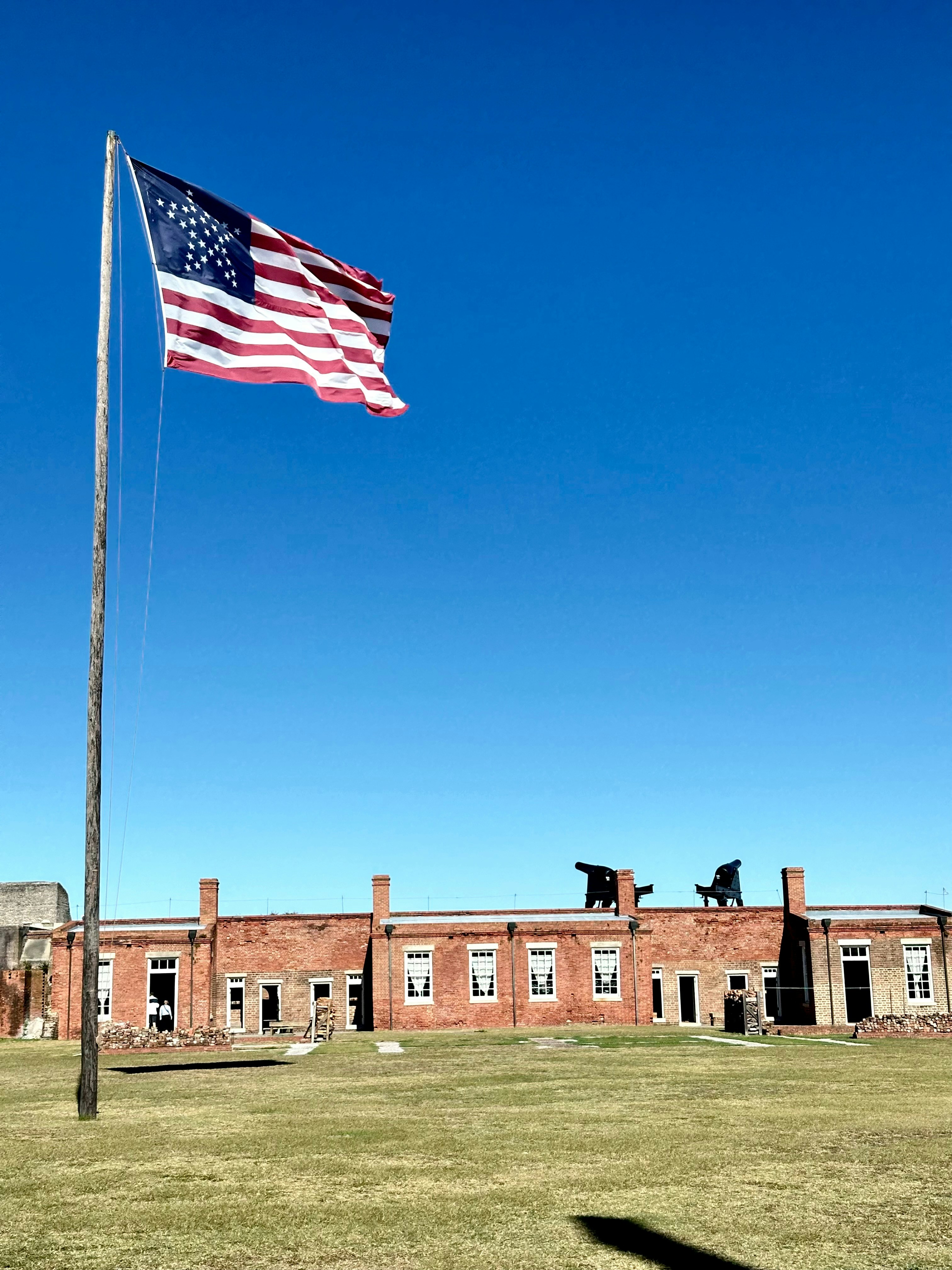 Flag Above a Quiet Brick Barracks: Rooftop Guardians Under a Clear Blue Sky