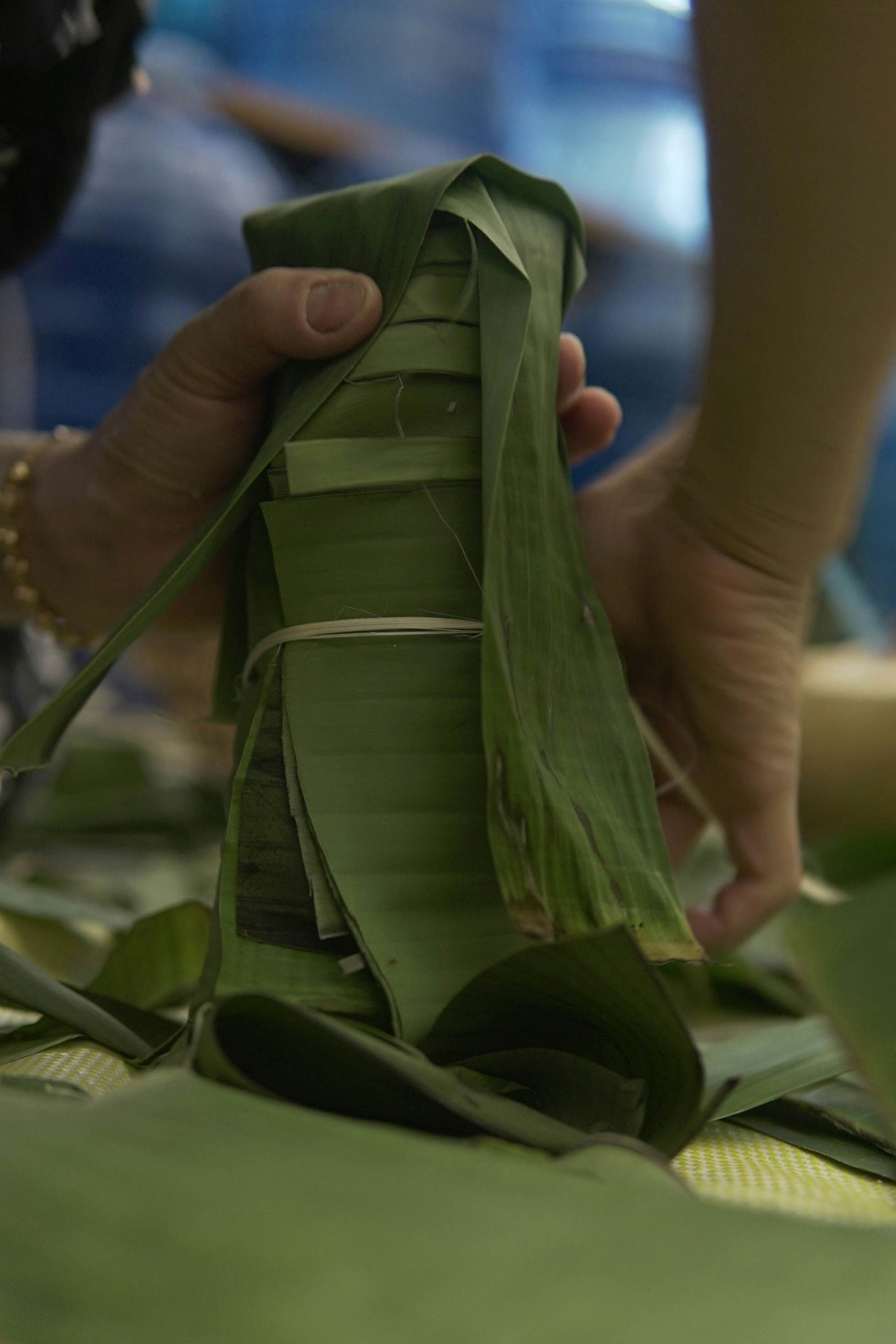 Leaf-wrapped Craft in Focus: Hands Shaping Green Bundles